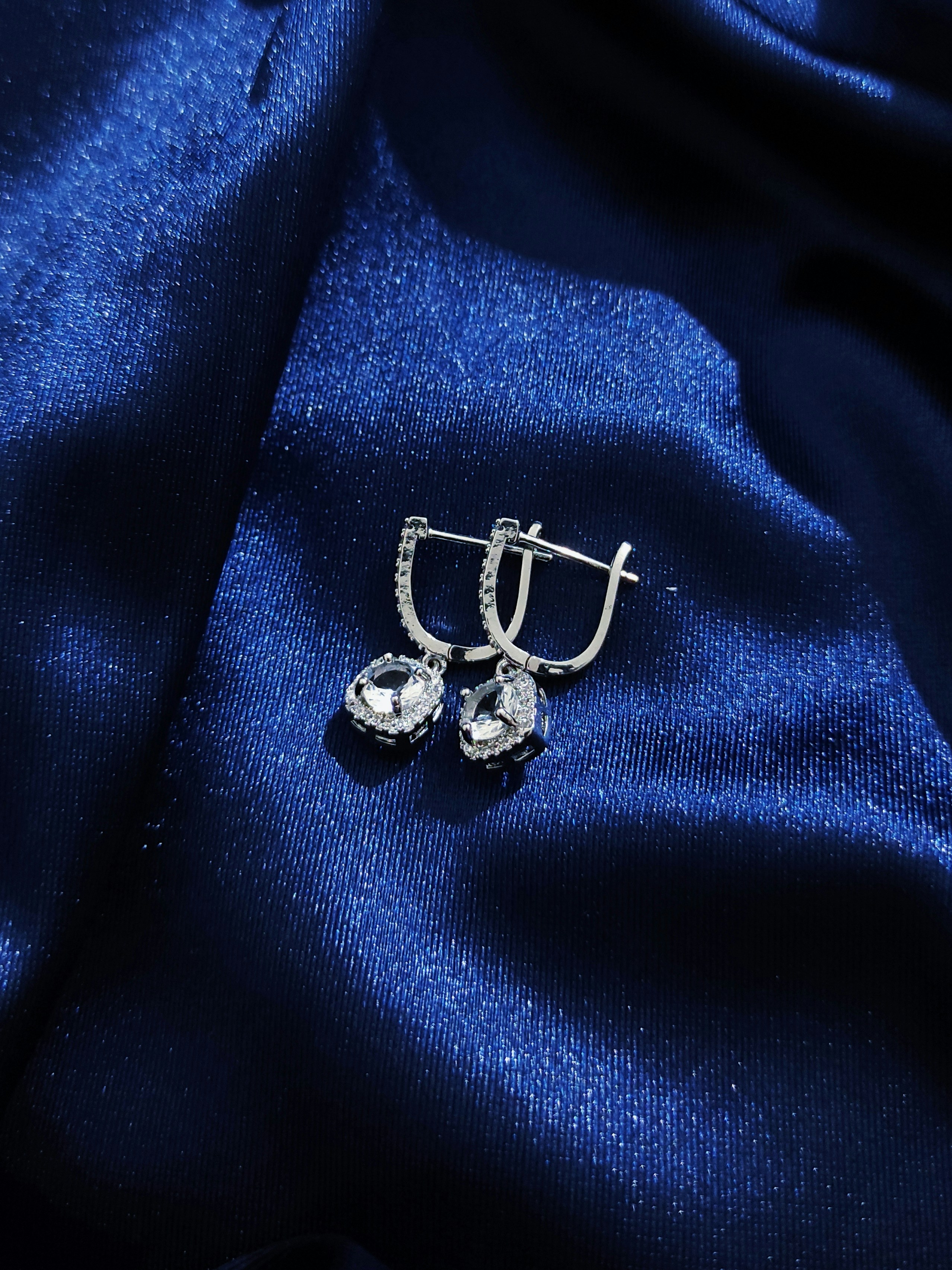 Sparkling earrings on a shiny, blue fabric.