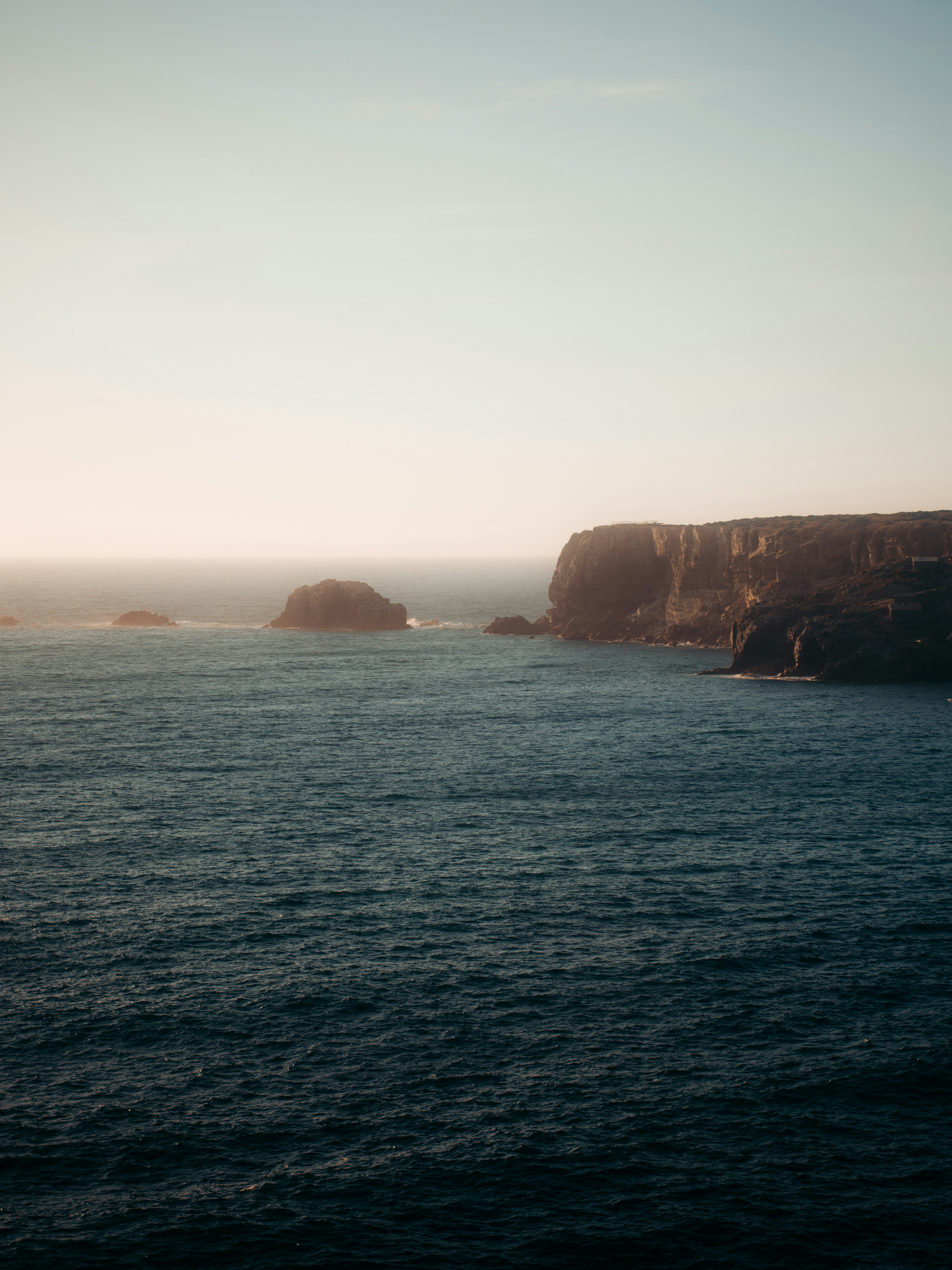 Cliffside overlooks a vast ocean under a hazy sky.