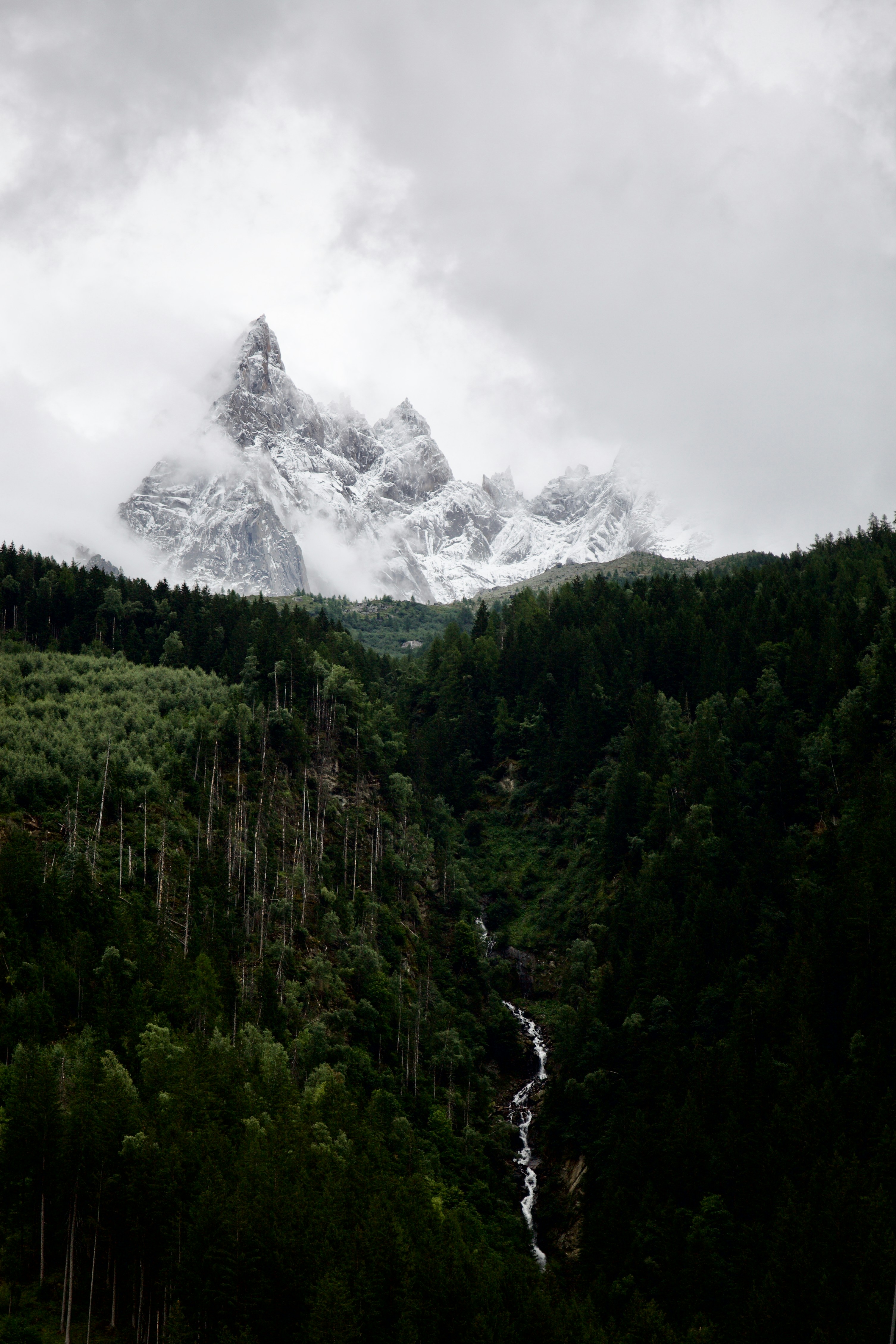 Majestic snow-capped peaks loom over a lush valley, with a gentle waterfall cascading through the greenery.