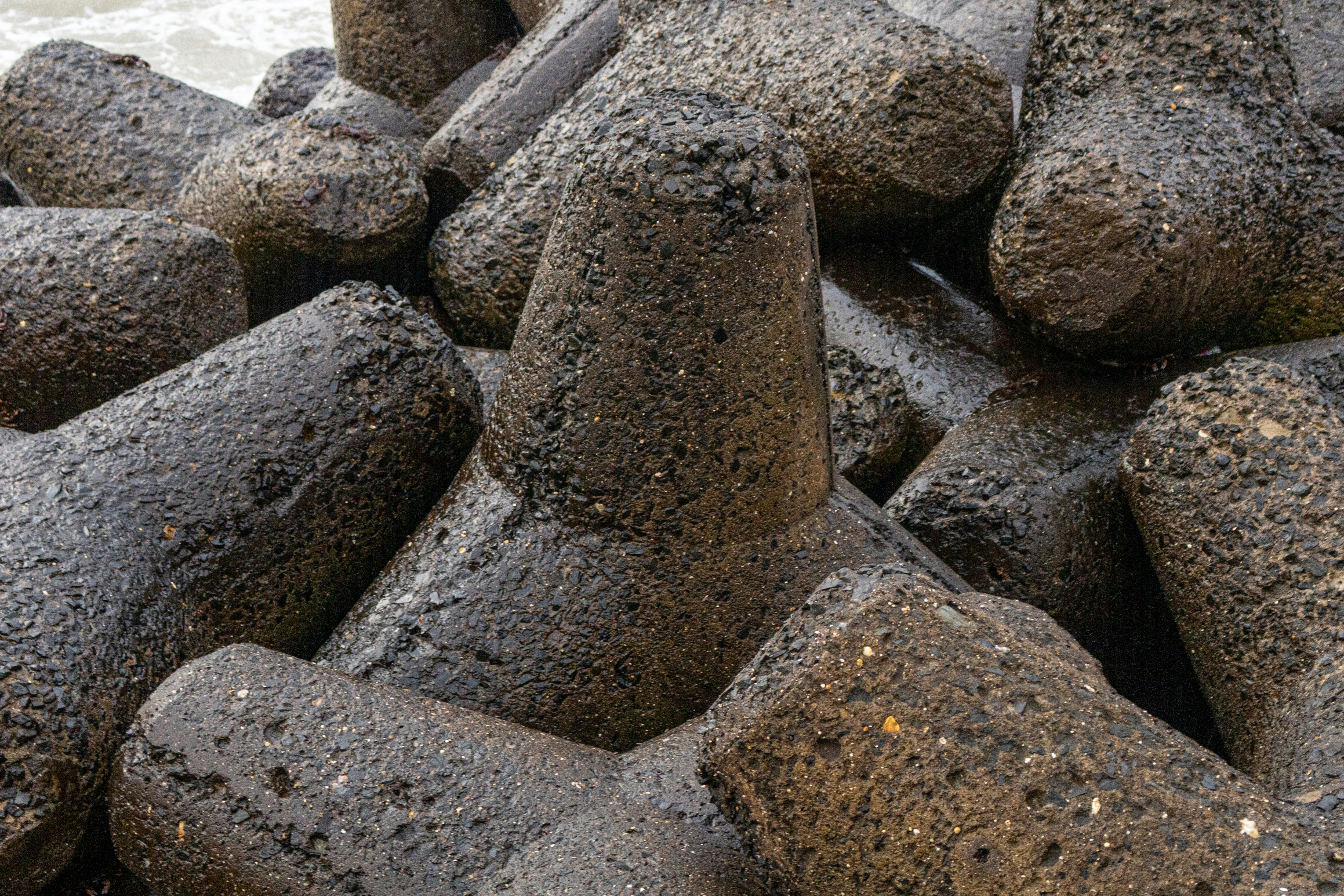 This image features the iconic tetrapods lining Marine Drive in Mumbai — four-legged concrete structures designed to absorb wave energy and protect the shoreline from erosion. Strategically placed along the coast, these geometric forms serve as both functional coastal defenses and recognizable visual elements of the city’s seafront. The photo captures their rough texture, interlocking design, and the rhythmic placement that defines Mumbai’s urban edge. These tetrapods symbolize the city's ongoing relationship with the Arabian Sea, blending civil engineering with a striking waterfront aesthetic | Concrete tetrapods form a coastal defense.