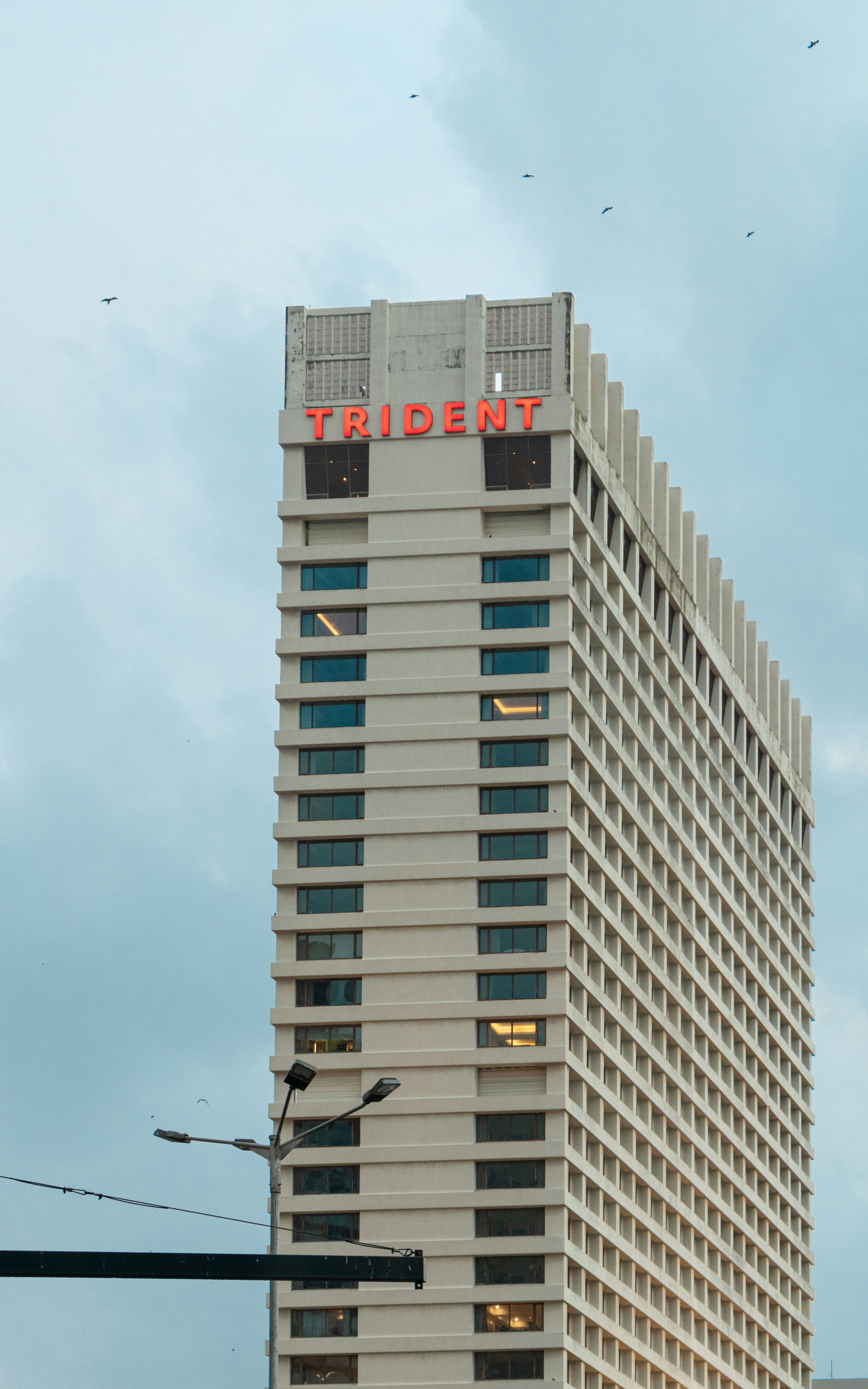 This image showcases the Trident Hotel in Nariman Point, Mumbai — a prominent luxury skyscraper along the city’s iconic coastline. The building’s clean vertical lines and modern architectural style reflect the elegance and commercial stature of South Mumbai’s business district. | The trident hotel tower stands tall under cloudy skies.