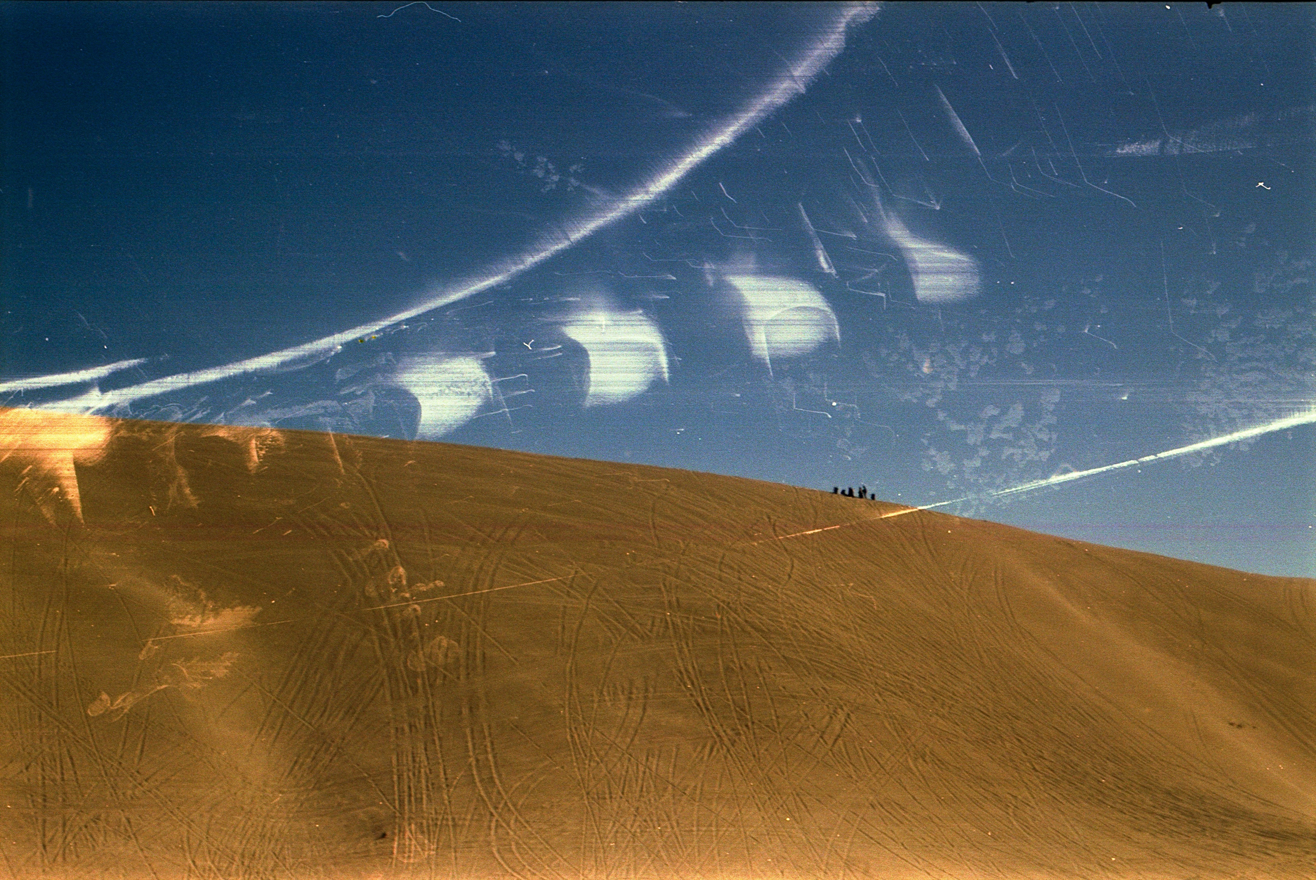 Dune Crest at Dusk: Tiny Figures Along a Ridge Beneath Curving Sky