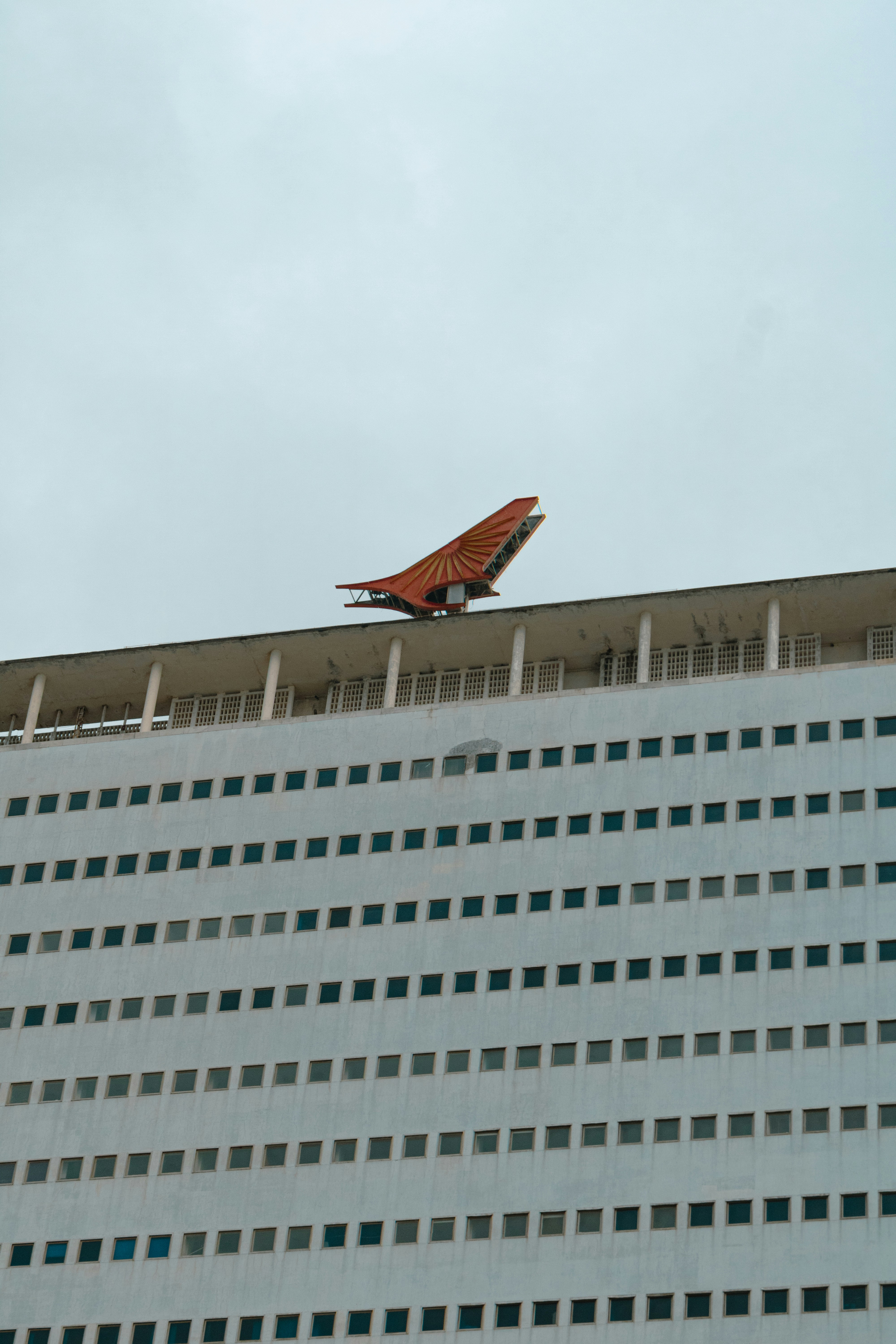 The Air India building, located in Mumbai's Nariman Point, is a prominent landmark with a rich history and unique architectural style. It was designed by John Burgee of the architectural firm Johnson/Burgee and completed in 1974. The building is known for its central air conditioning, one of the first in India to feature this, and for its escalators, which were also a novelty at the time. | A unique roof ornament tops a white building.