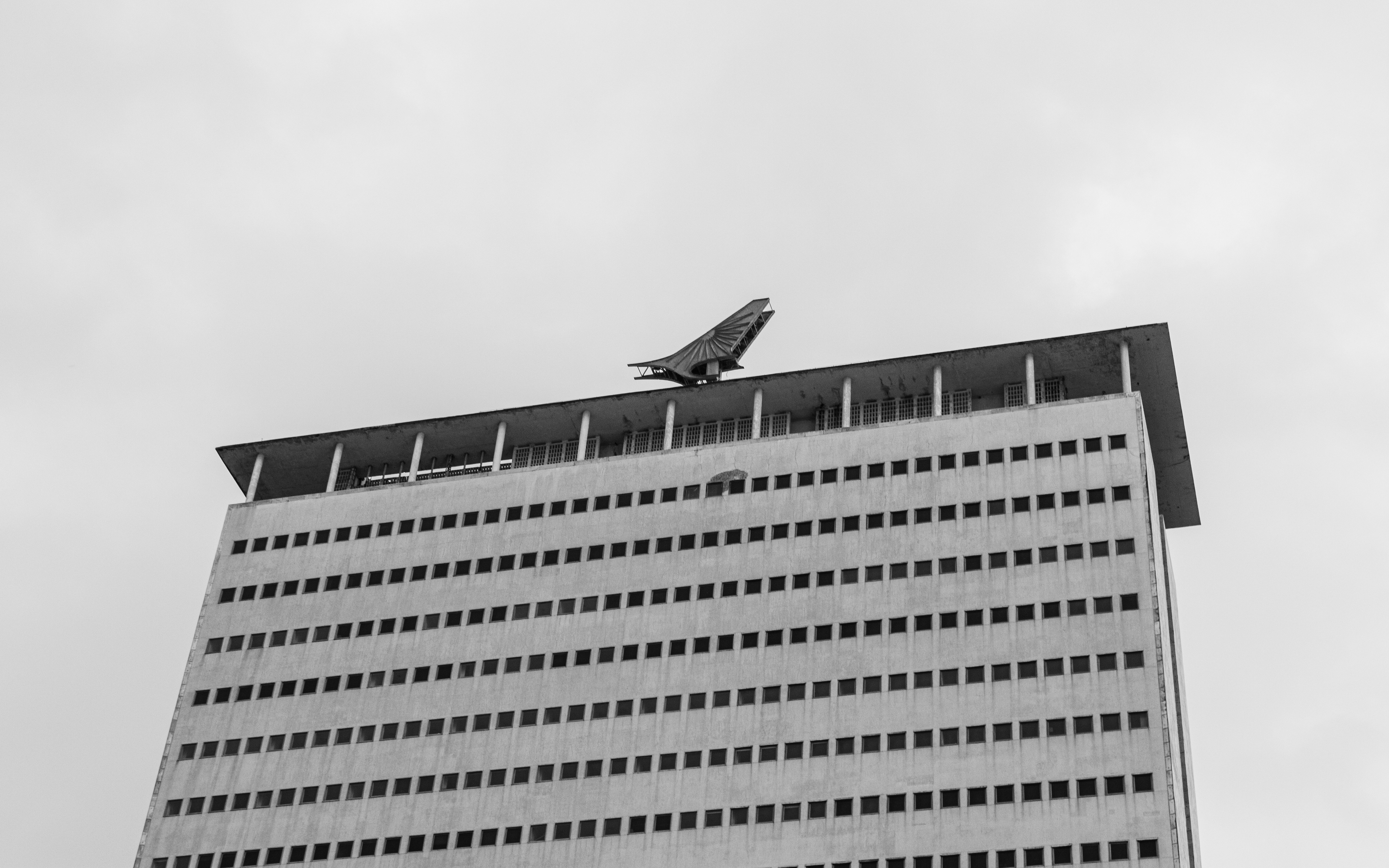 The Air India building, located in Mumbai's Nariman Point, is a prominent landmark with a rich history and unique architectural style. It was designed by John Burgee of the architectural firm Johnson/Burgee and completed in 1974. The building is known for its central air conditioning, one of the first in India to feature this, and for its escalators, which were also a novelty at the time. | An airplane-shaped structure sits atop a tall building.