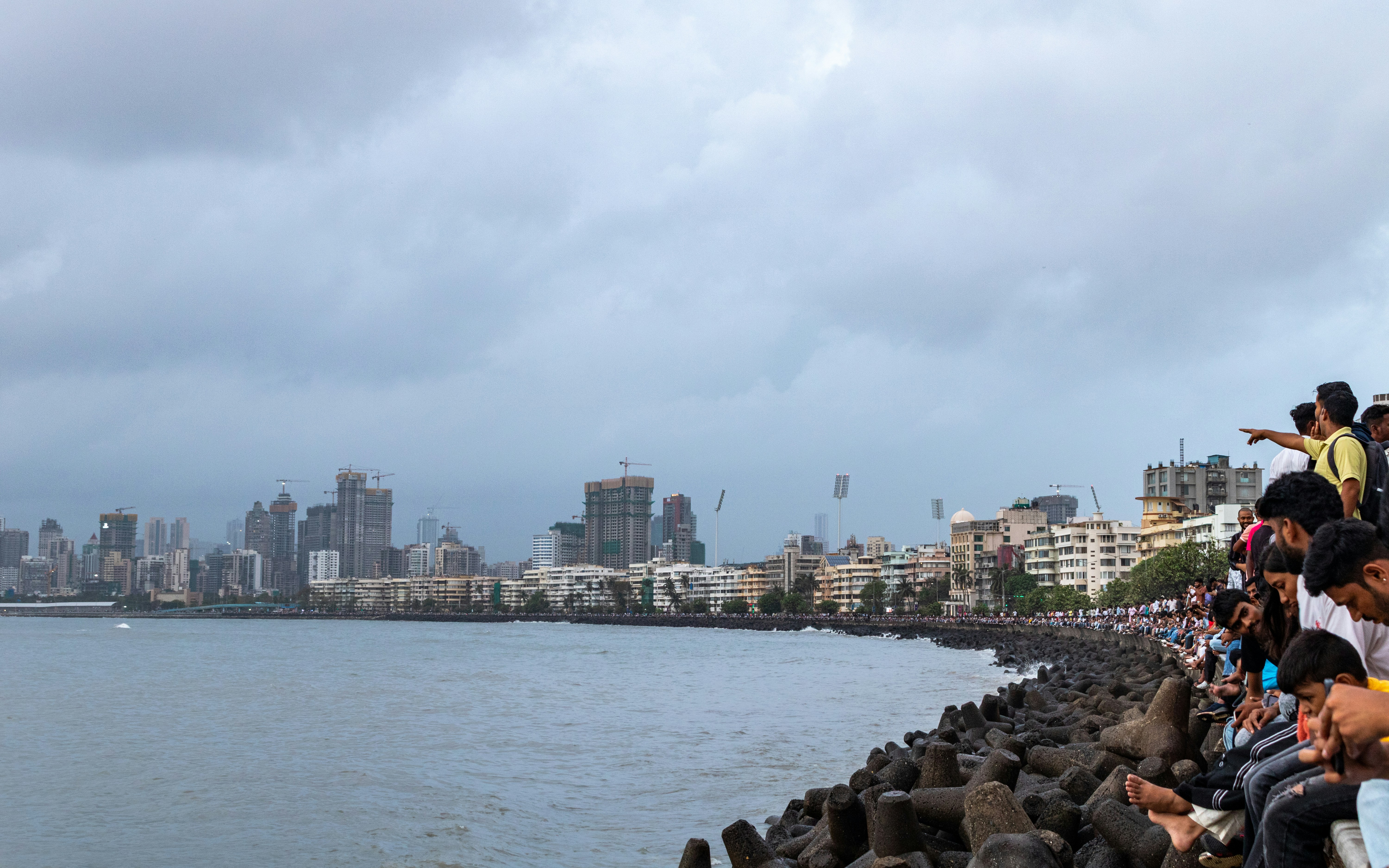 Crowd Along the Breakwater Framing a Distant City Skyline