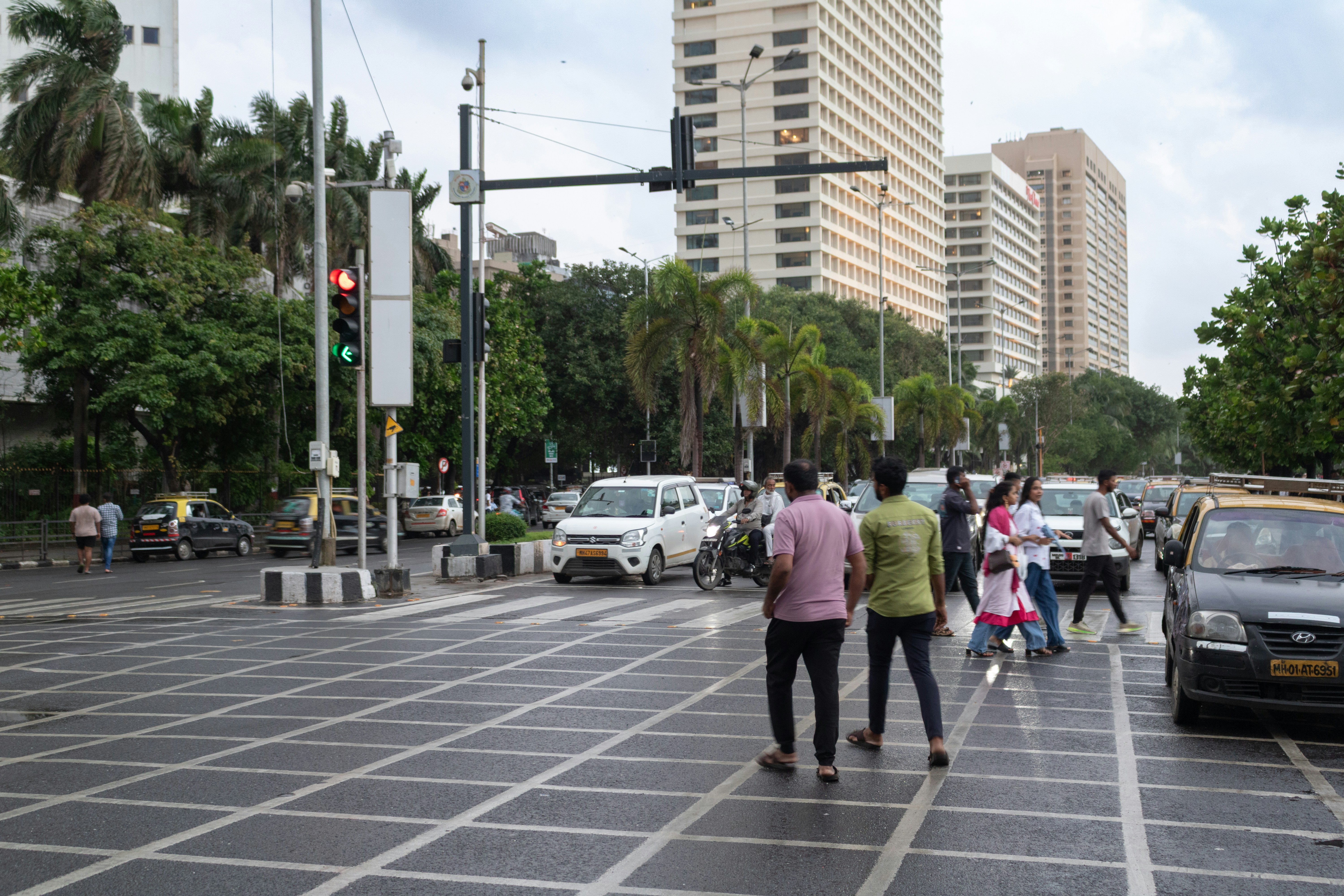 Pedestrians casually cross the road at Nariman Point, Mumbai, as cars wait at a red traffic light. | People walk on a city street, near buildings.