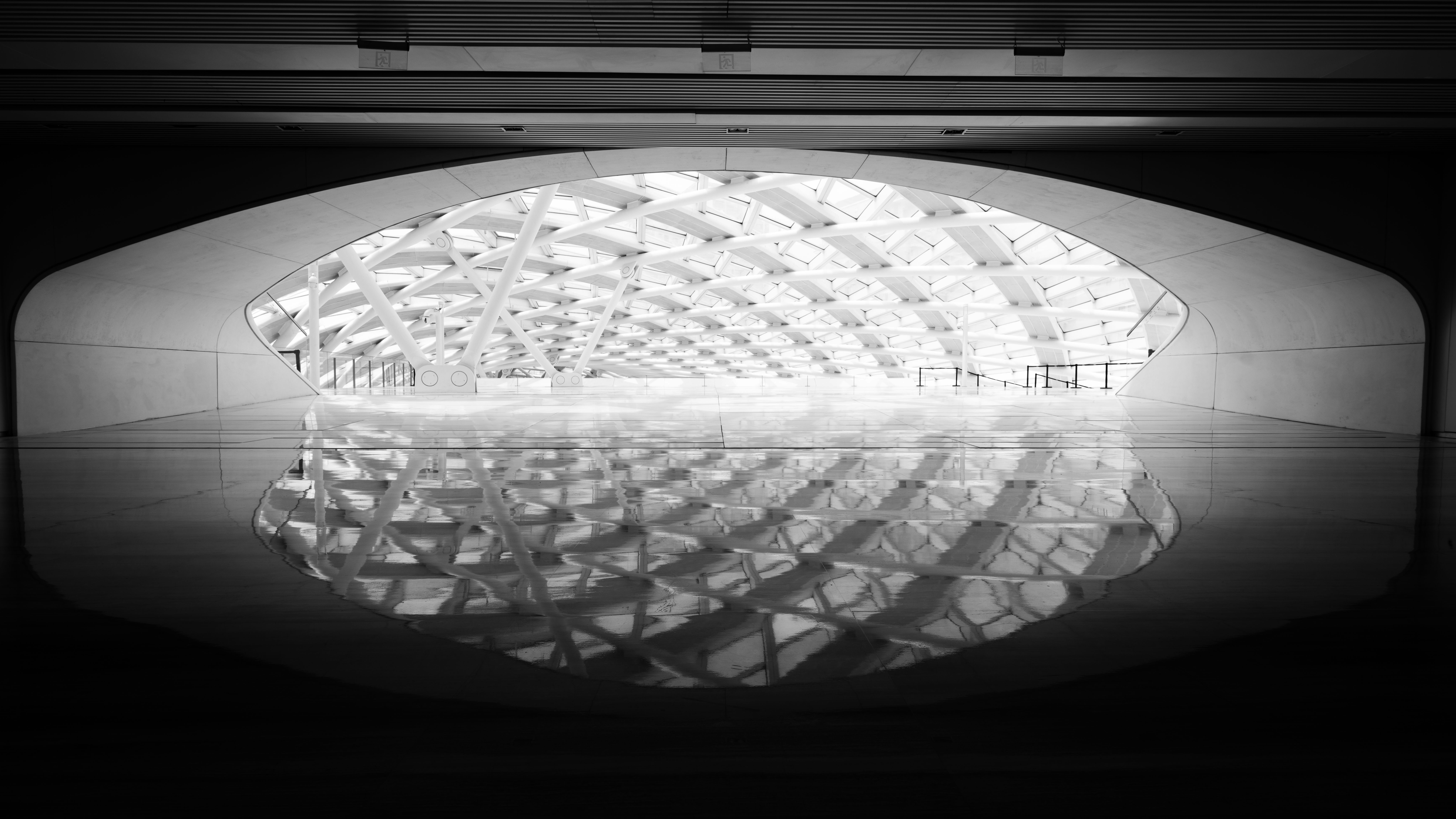 A modern architectural space featuring intricate lattice structures and a reflective floor, creating a striking visual symmetry.