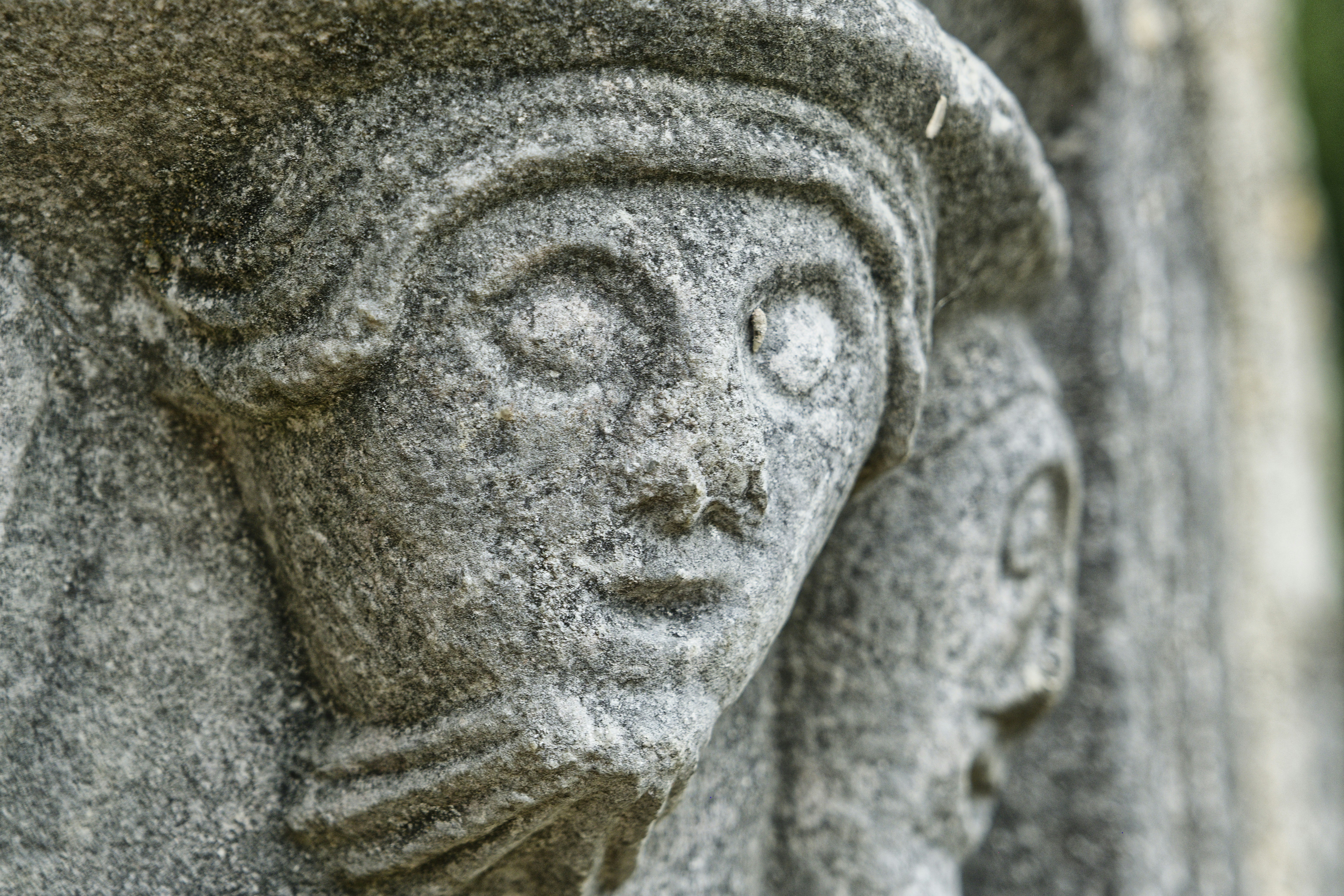 Historical stone carving depicting human figures with intricate details in a serene outdoor setting during the afternoon - Close-up of an ancient stone carving revealing expressive human faces. The intricate details showcase craftsmanship, highlighting a rich cultural heritage in an outdoor setting. | Stone carving of a face with hat.