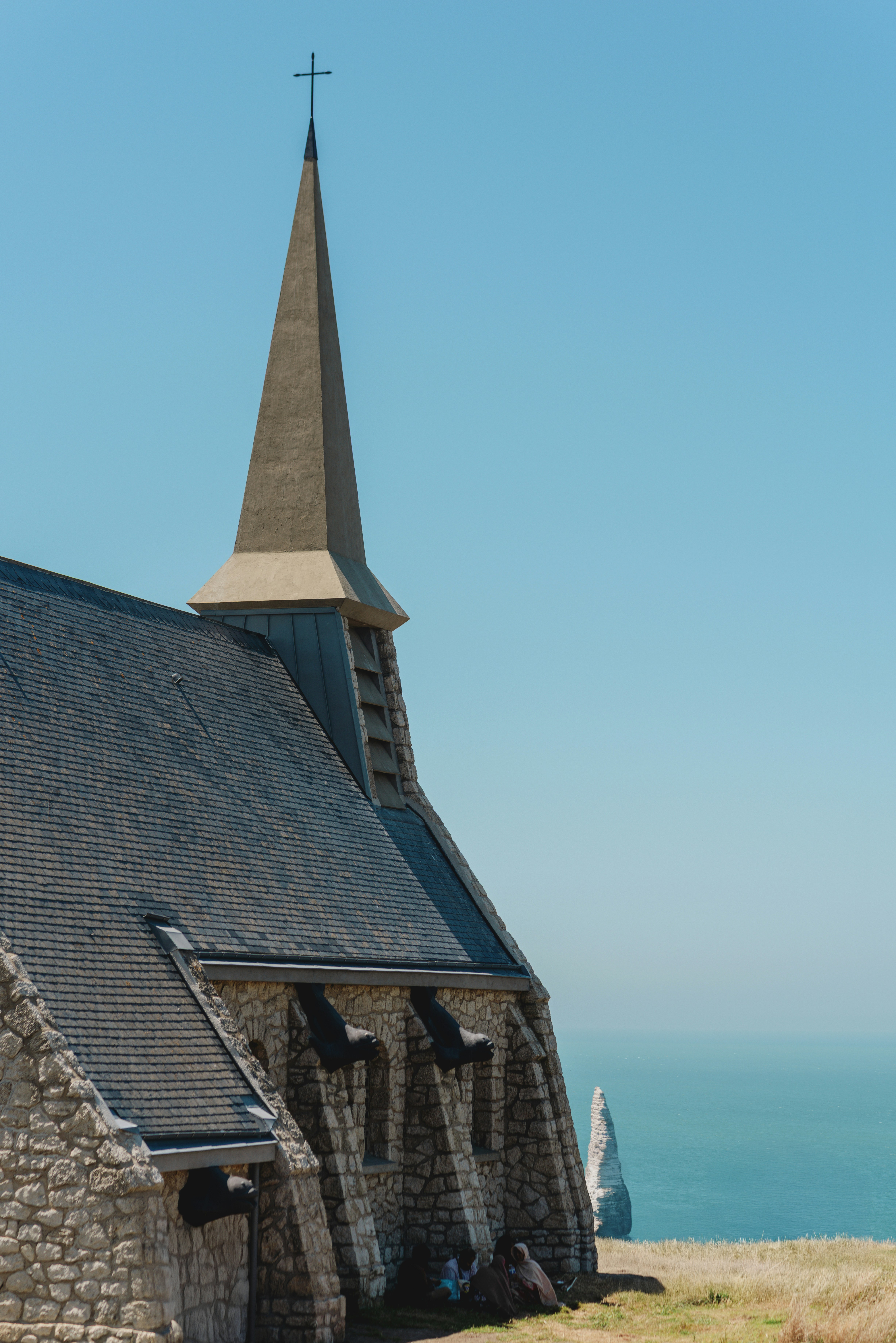 Historic church stands against a backdrop of the ocean and a distant rock formation. The architecture features a prominent steeple and stone facade.