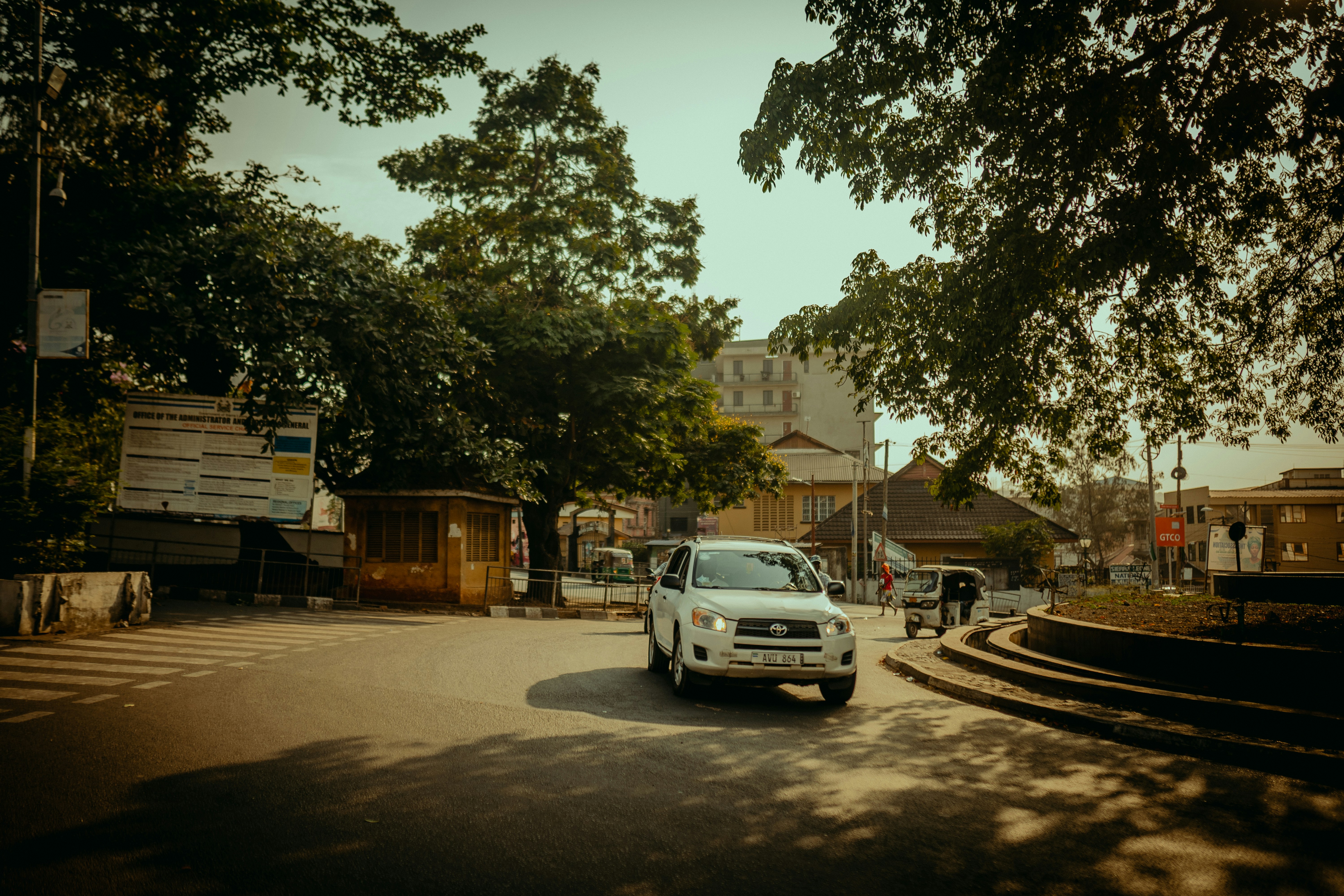 A car drives through a tree-lined street.