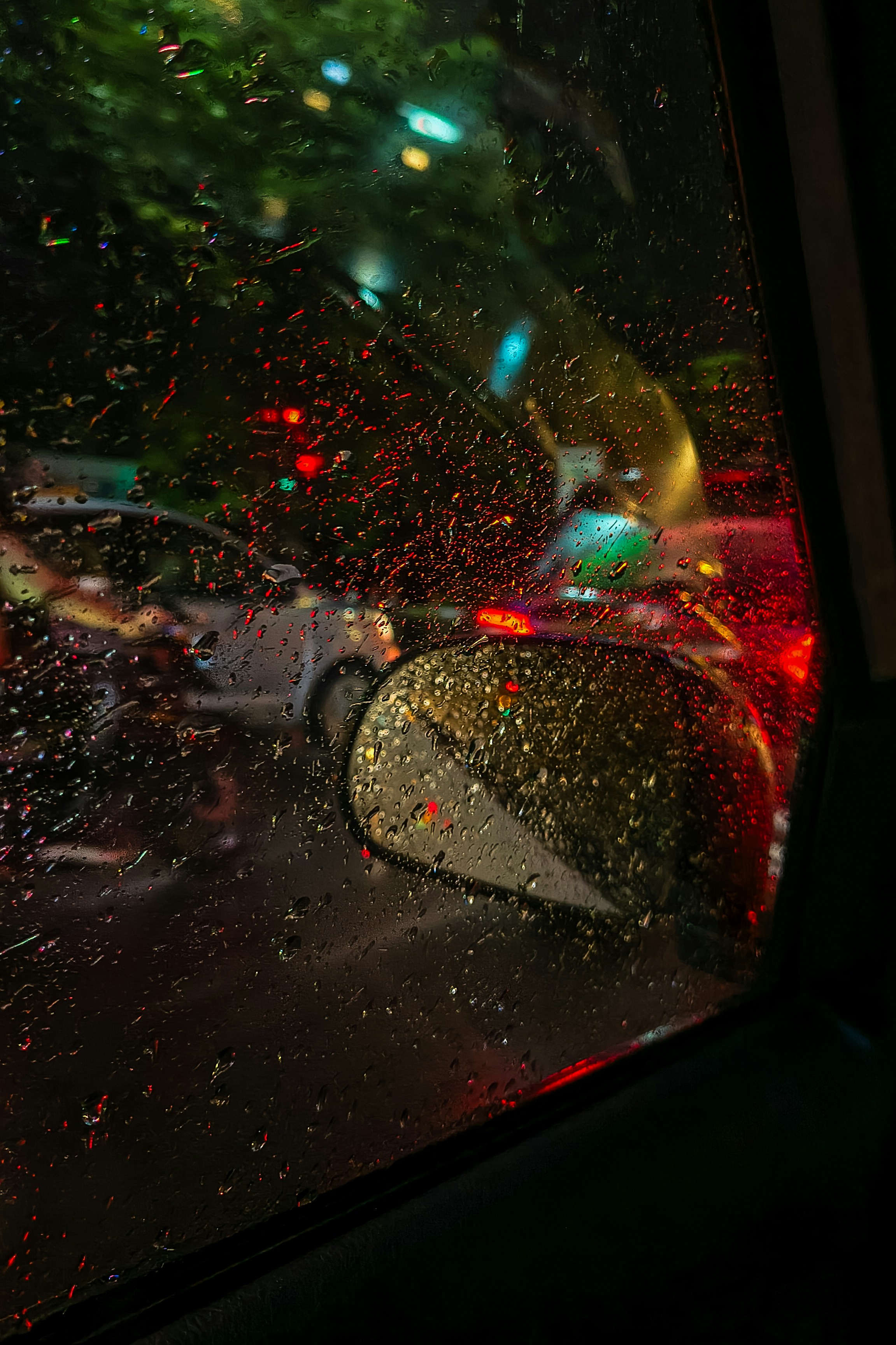 Raindrops cling to a car window, distorting the vibrant lights of a bustling city street at night.