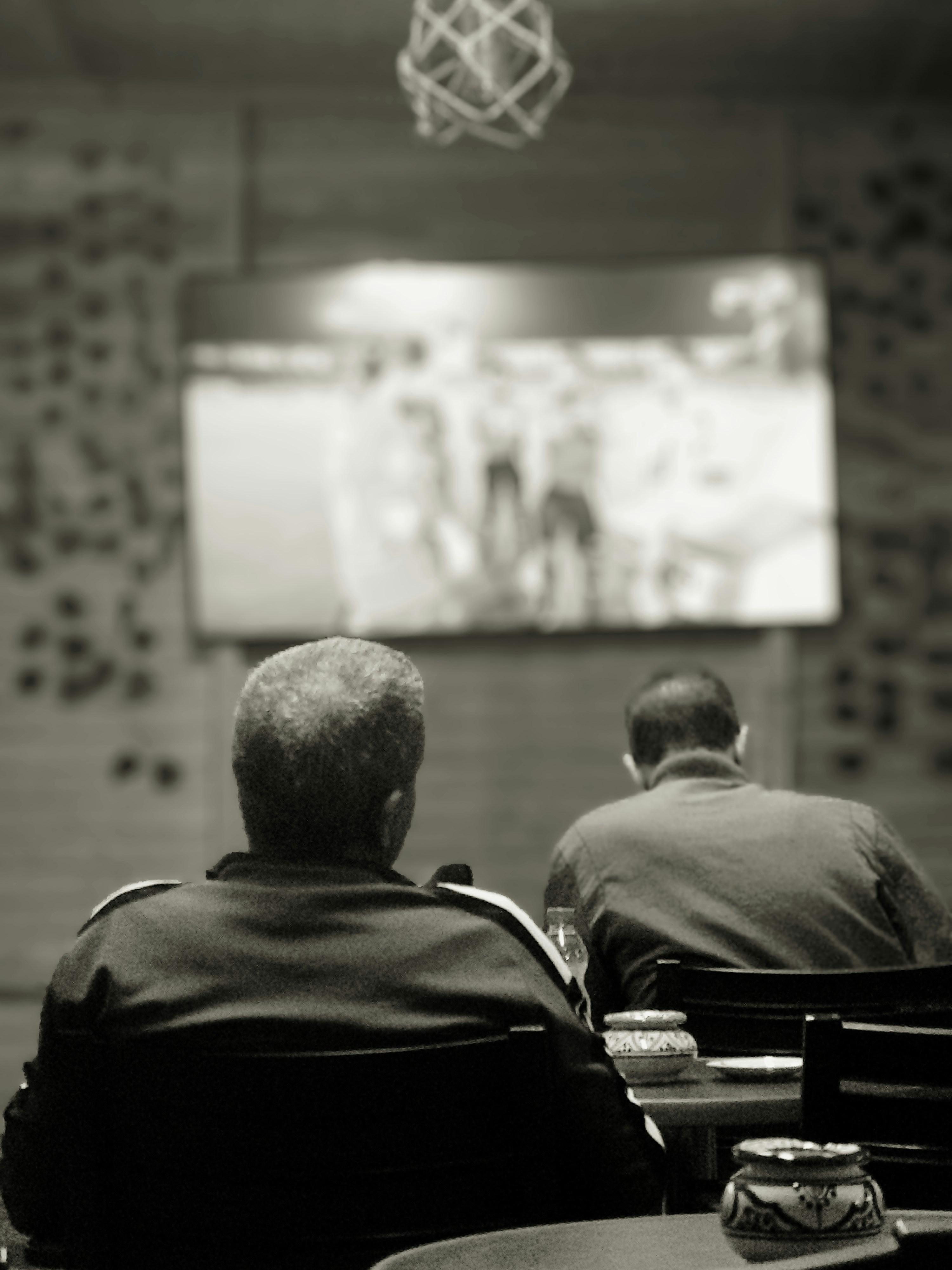 Two men watch a screen in a restaurant.