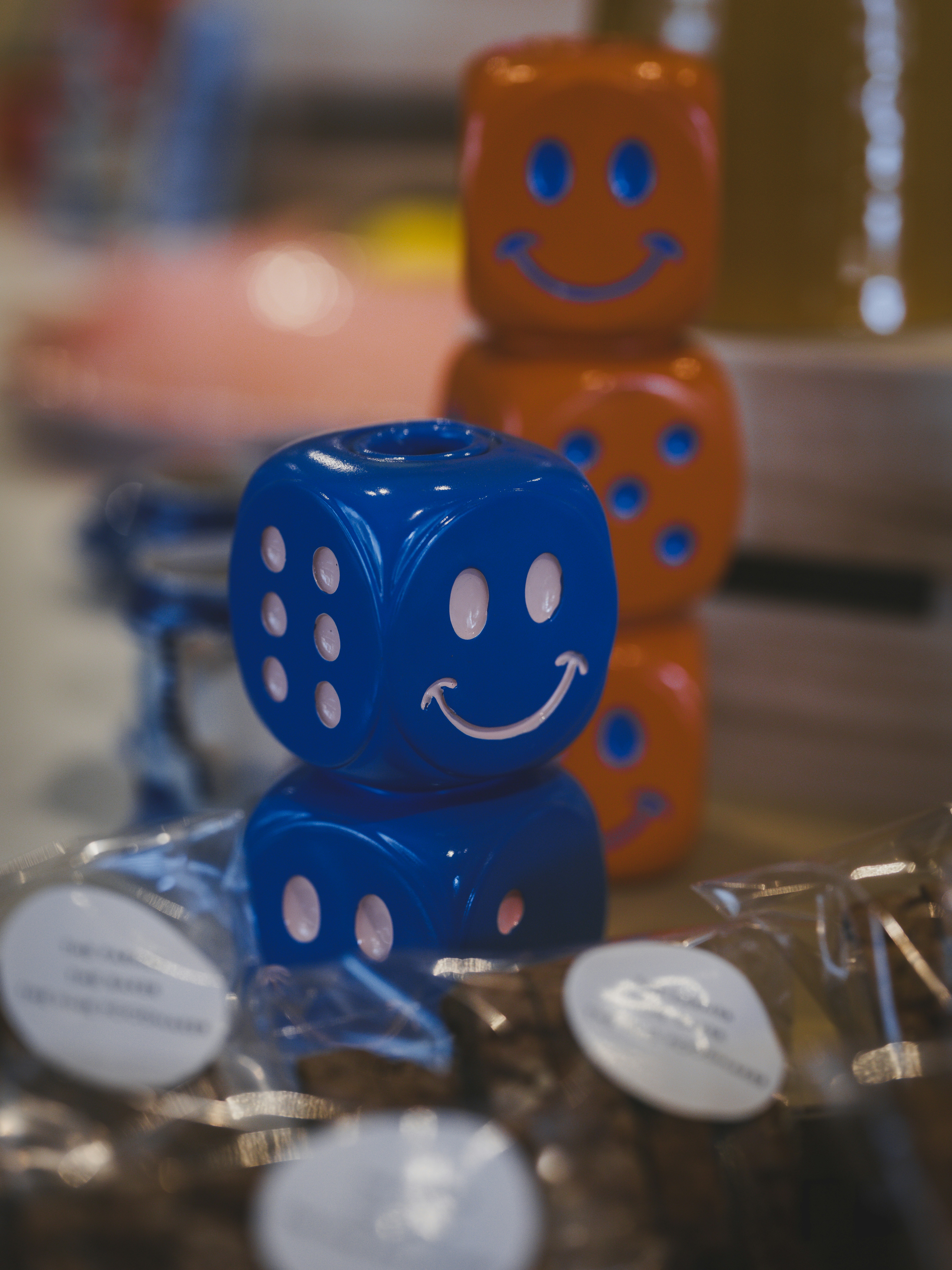 Bright blue and orange dice with smiley faces stacked playfully, surrounded by various colorful items. A whimsical display of joy and fun.