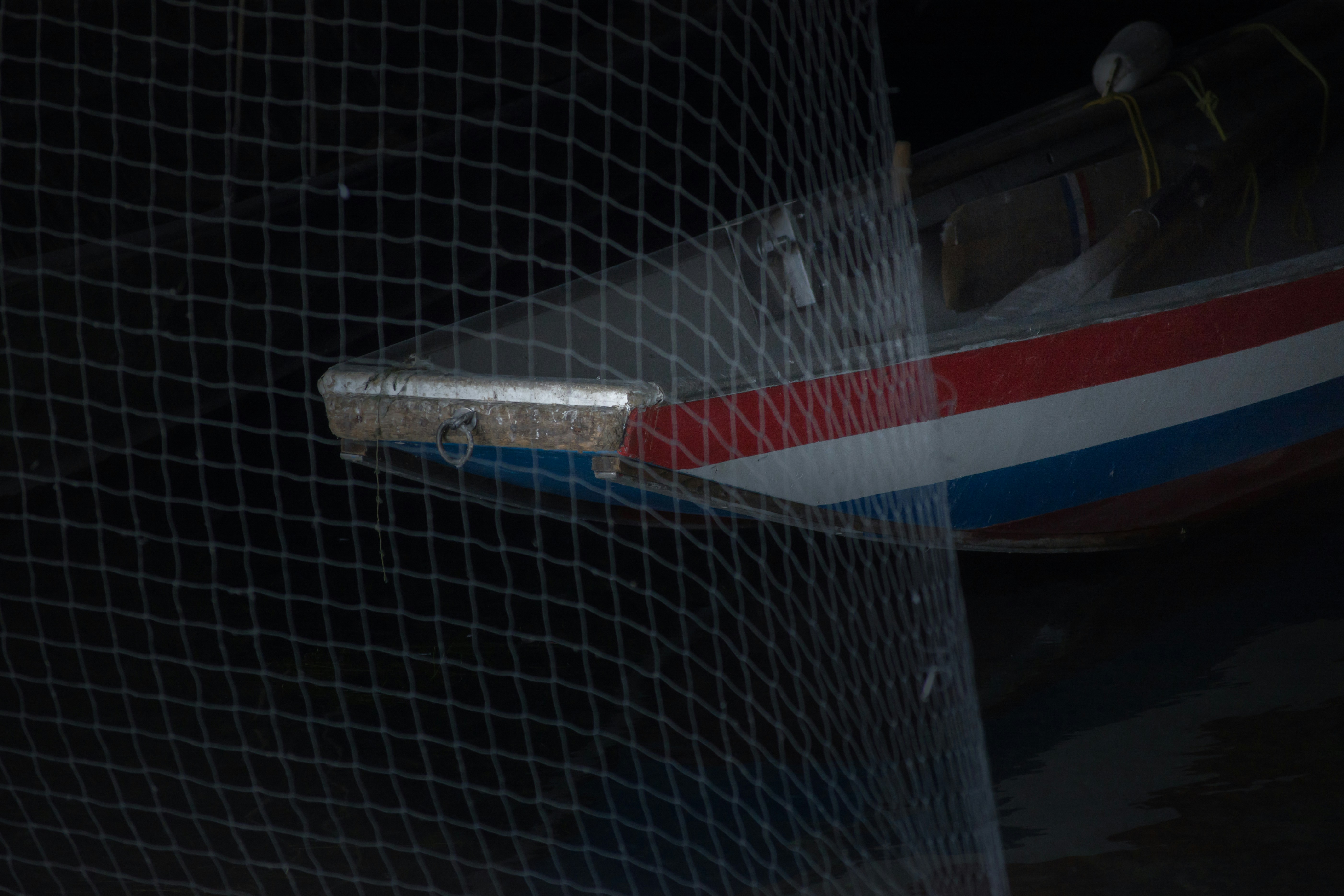 A colorful boat partially obscured by a fishing net, creating an intriguing interplay of textures and colors against a dark backdrop.