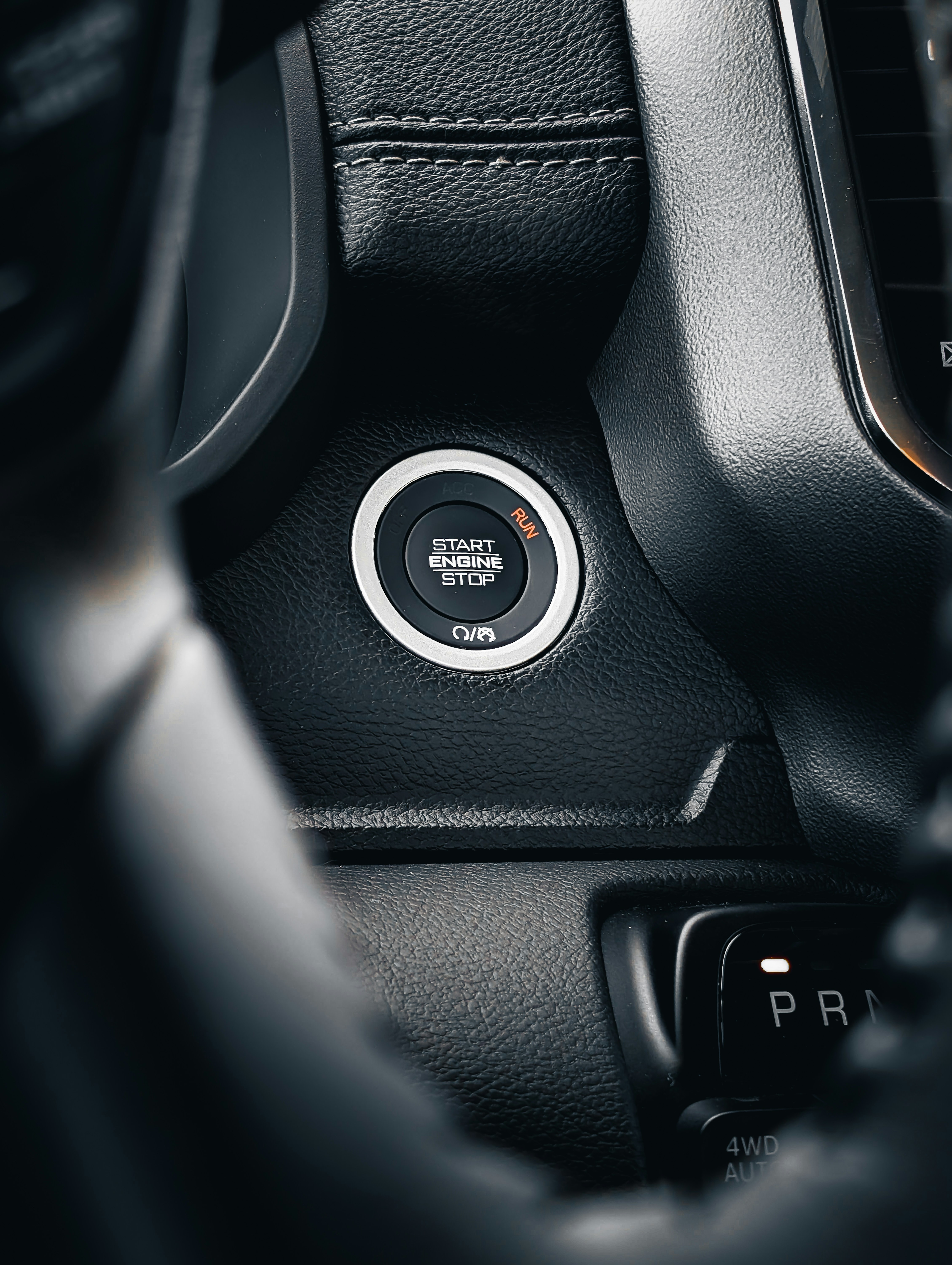 This striking close-up perfectly frames a sophisticated "START ENGINE STOP" push-button, elegantly set within a textured black leather car interior, symbolizing modern automotive technology and effortless vehicle operation. | Engine start button is shown inside a car.