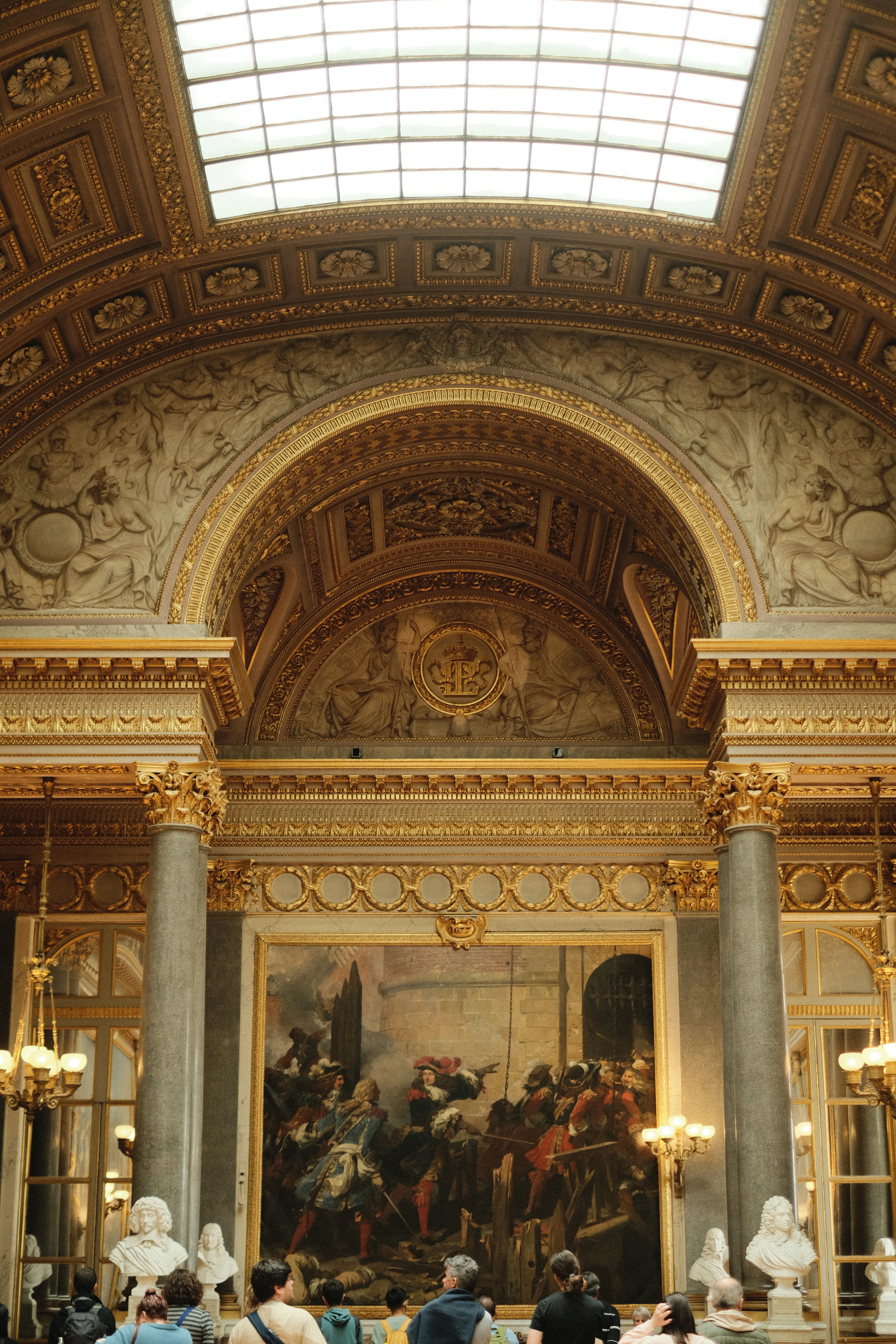 Opulent interior of a historic gallery showcasing a large painting and intricate architectural details, with visitors admiring the art.