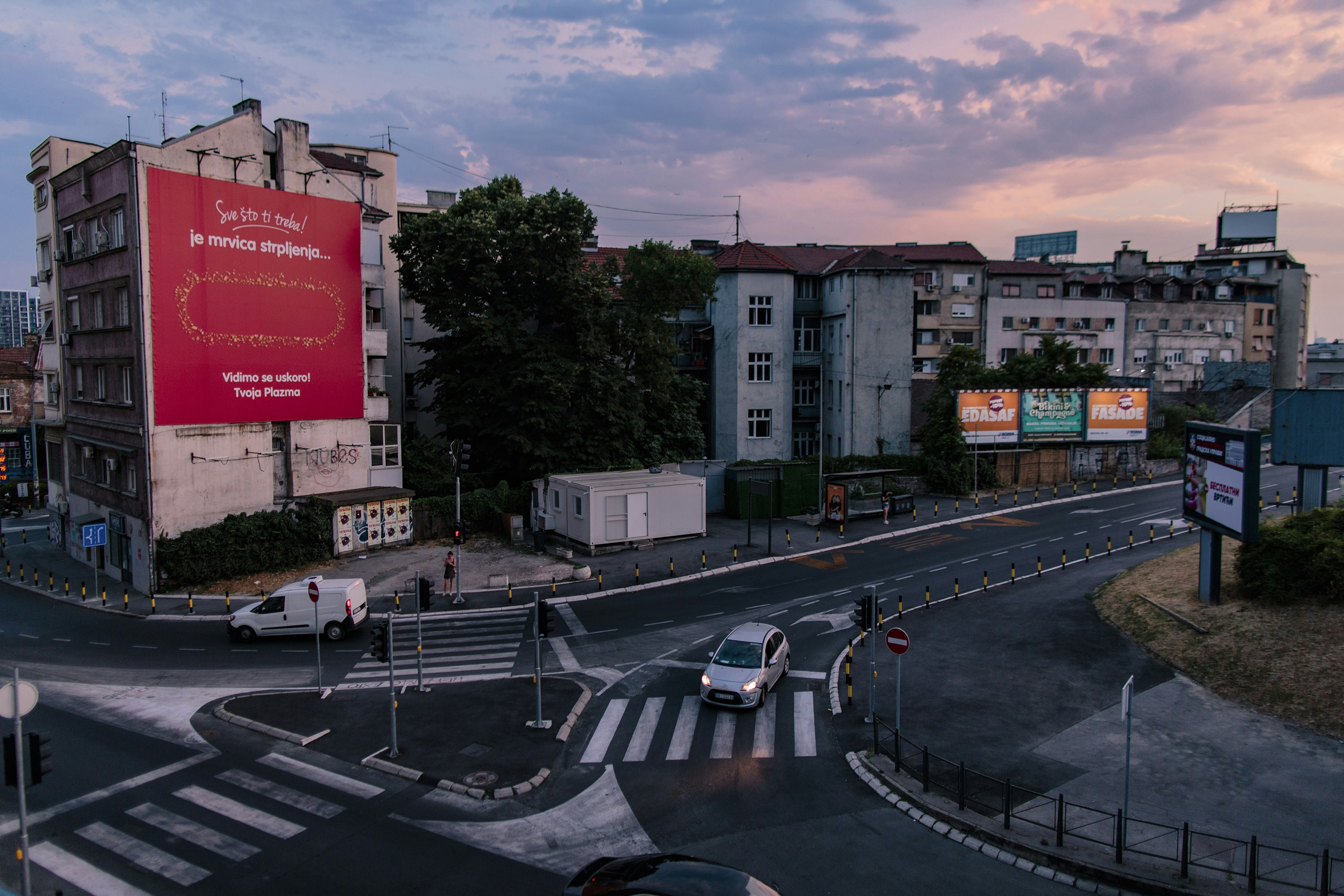 A city street corner with cars and billboards.
