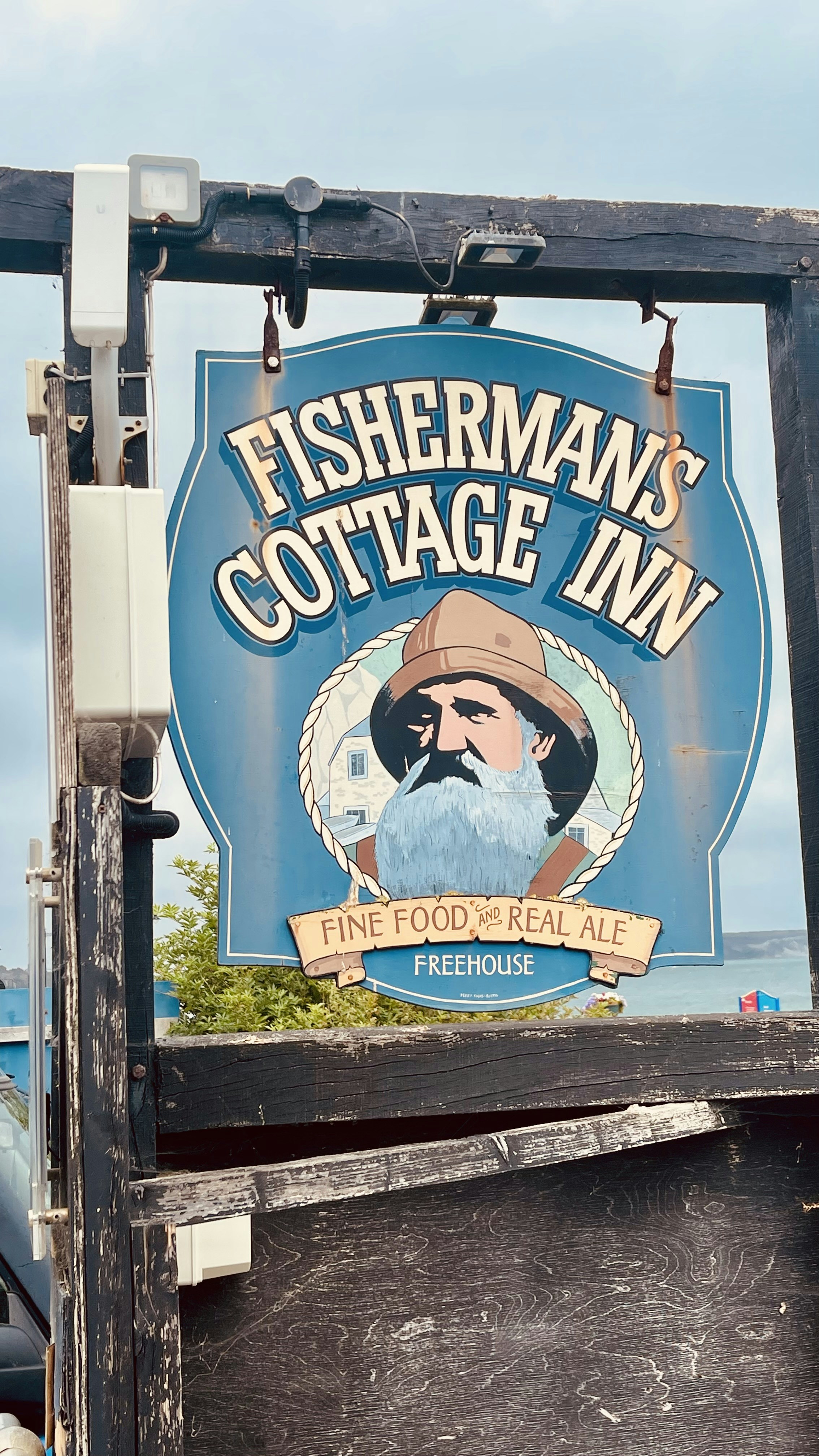 Sign of the Fisherman’s Cottage in on beach | The fisherman's cottage inn sign is displayed.