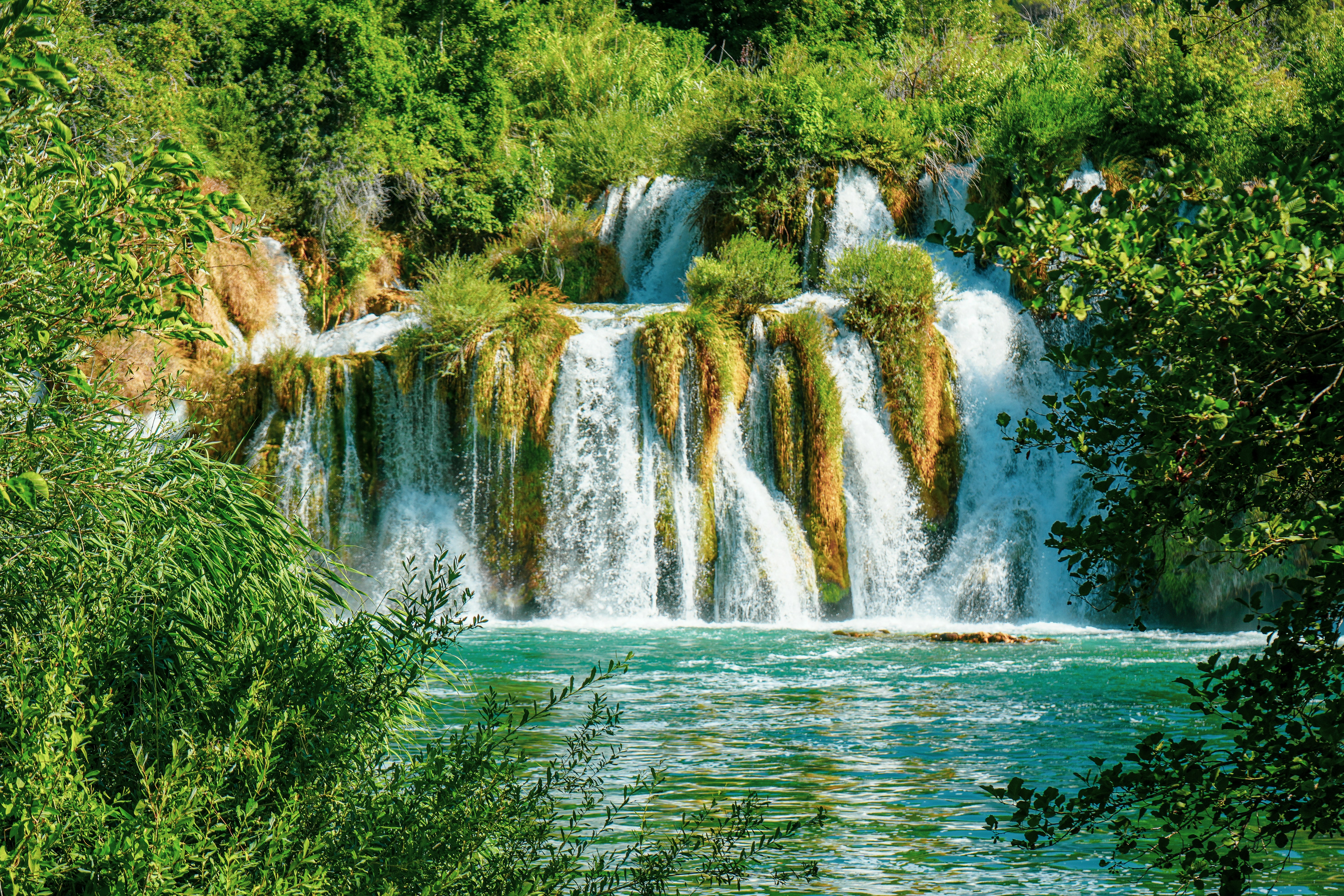 Lush greenery surrounds a vibrant waterfall cascading into a serene turquoise pool, showcasing the beauty of nature's harmony.