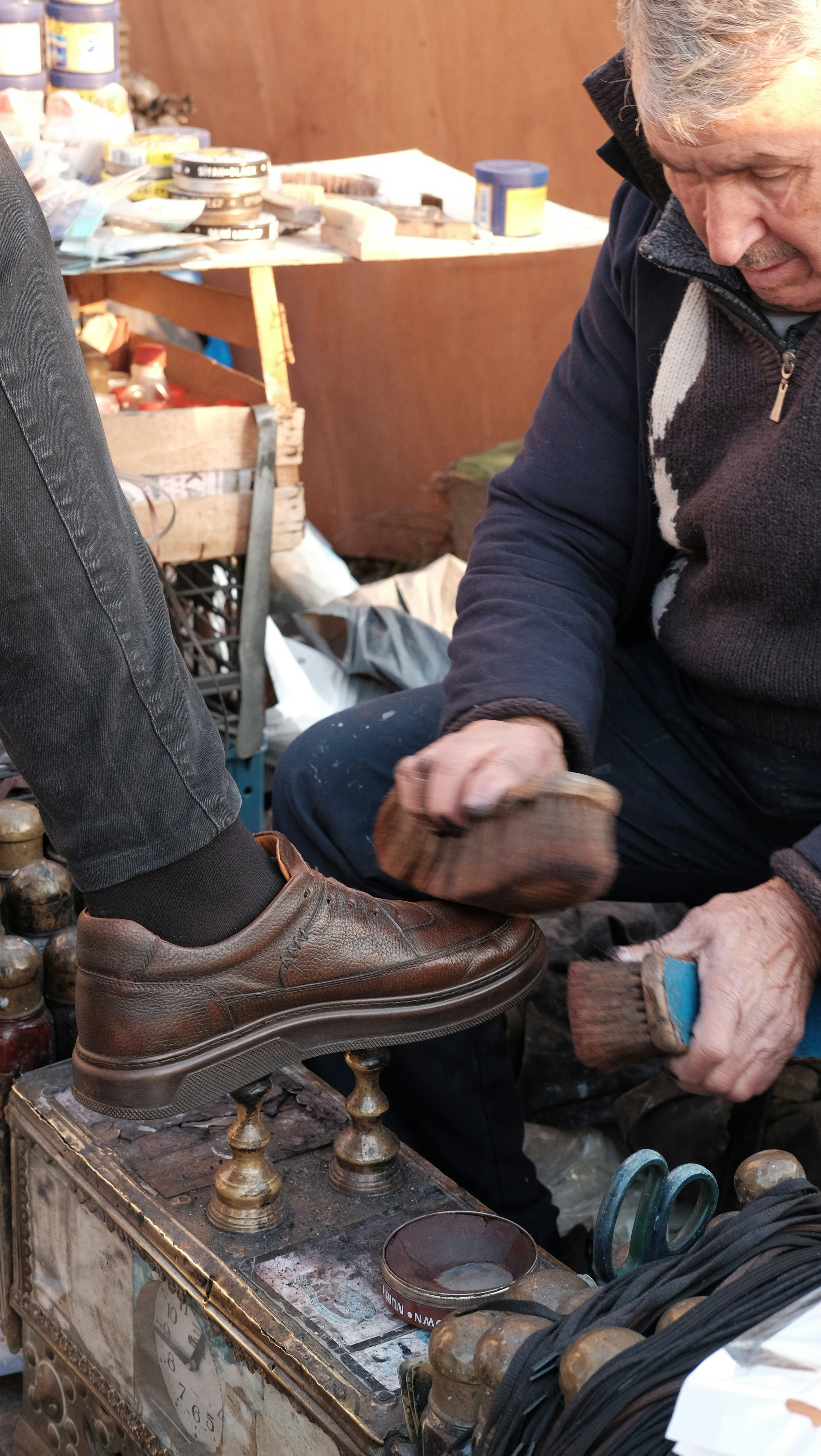 A candid moment captured in the heart of Istanbul — a traditional shoeshiner at work, bringing life back into a pair of well-worn leather shoes. Surrounded by brushes, polish tins, and decades of craftsmanship, this image tells a quiet story of dedication, timeless skill, and the beauty of everyday rituals in a bustling city.