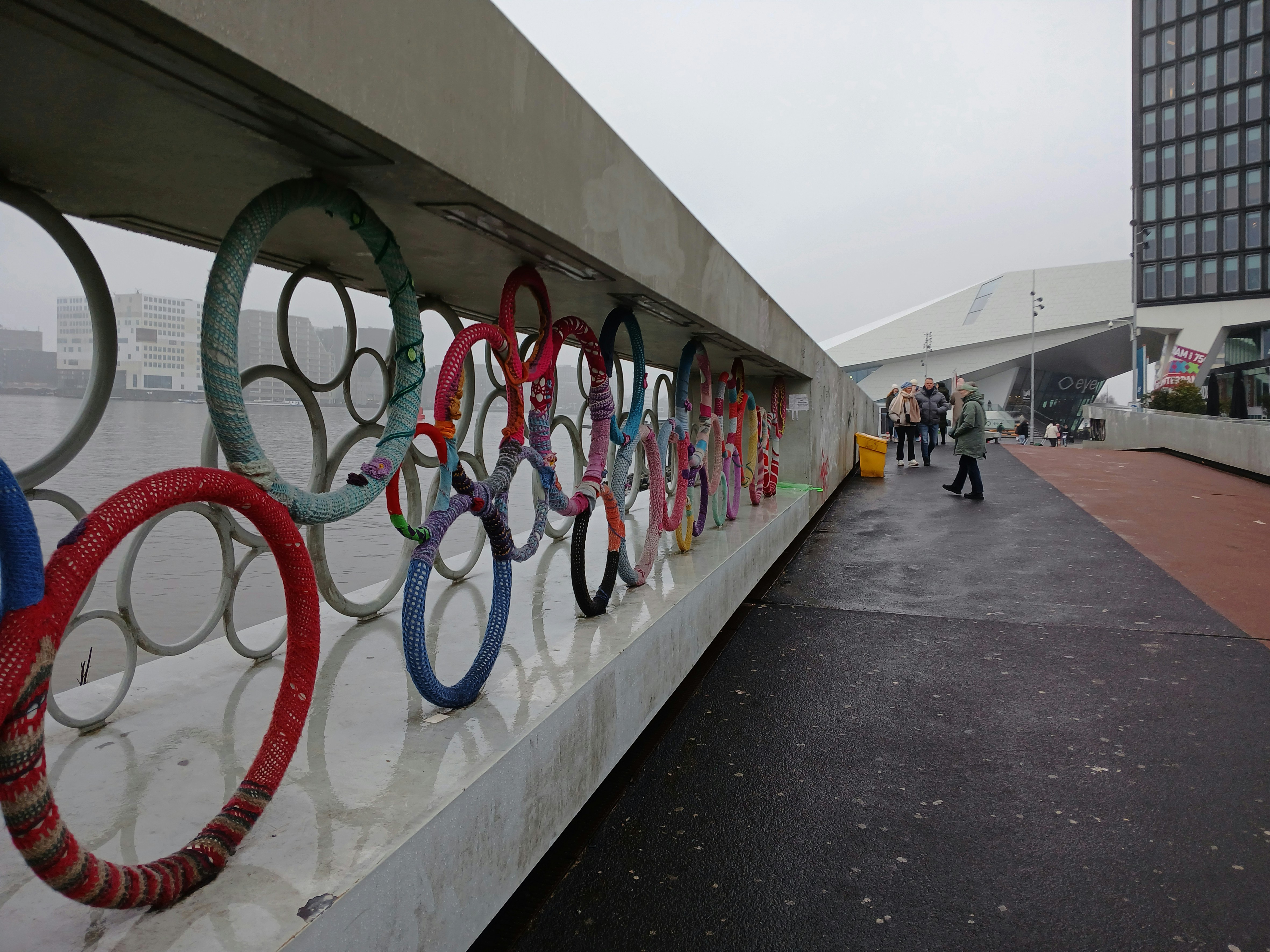 Free download photo high resolution of a grey view over the sidewalk and bike path along the river IJ in city Amsterdam-North A grey day in February. Street photography free image in high resolutions by Fons Heijnsbroek, The Netherlands Dutch photo / Gratis download foto in hoge resolutie van een grijs uitzicht over de stoep en het fietspad langs het IJ in Amsterdam-Noord / Overhoeks. Een grijze dag in februari. Straatfotografie, gratis afbeelding in hoge resolutie door Fons Heijnsbroek, Nederland. Nederlandse foto. | Colorful rings decorate a railing along a walkway.