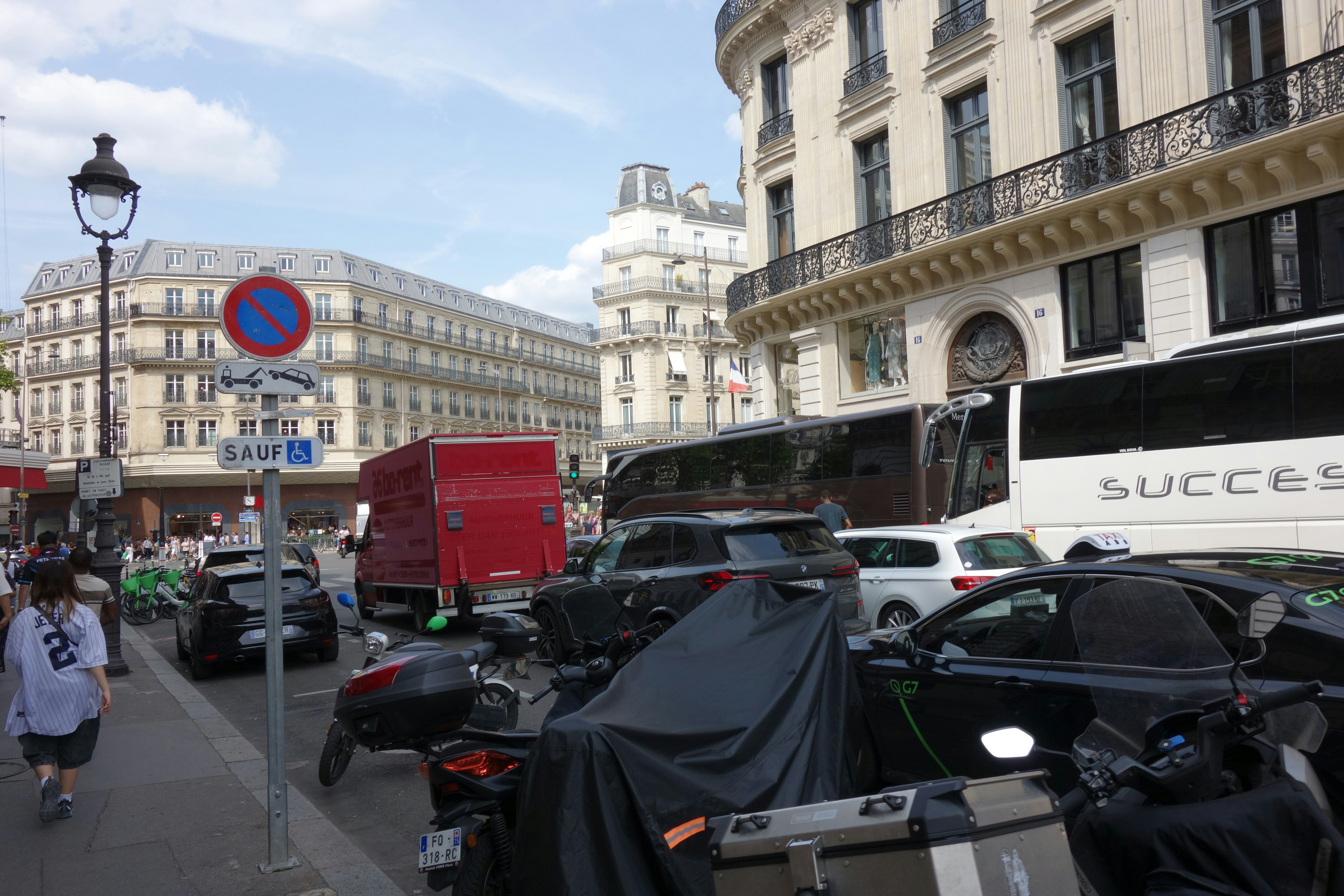 Busy street scene in an urban setting, showcasing a mix of vehicles and pedestrians amidst historic architecture.