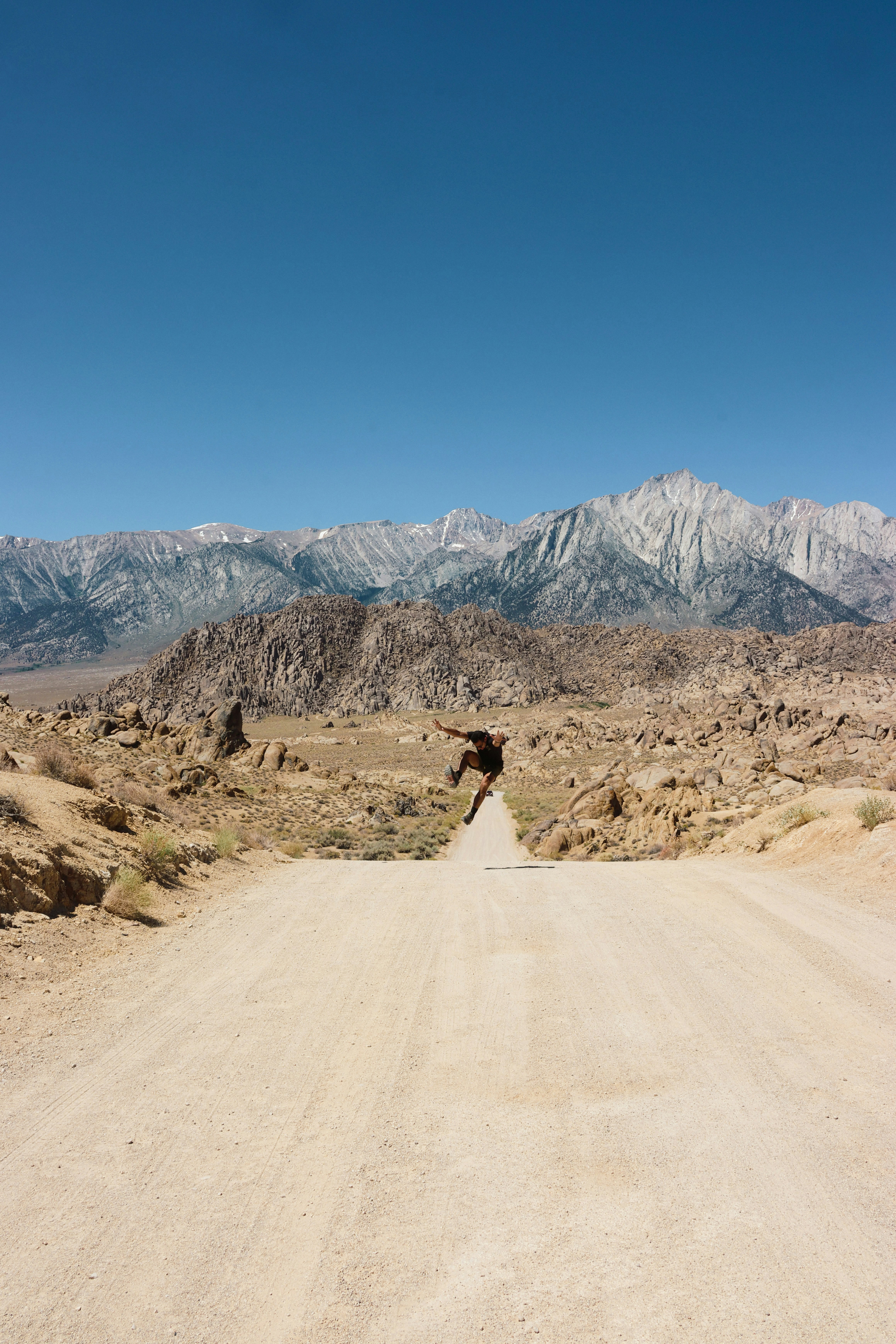 Life’s good | A person jumps on a desert road with mountains.