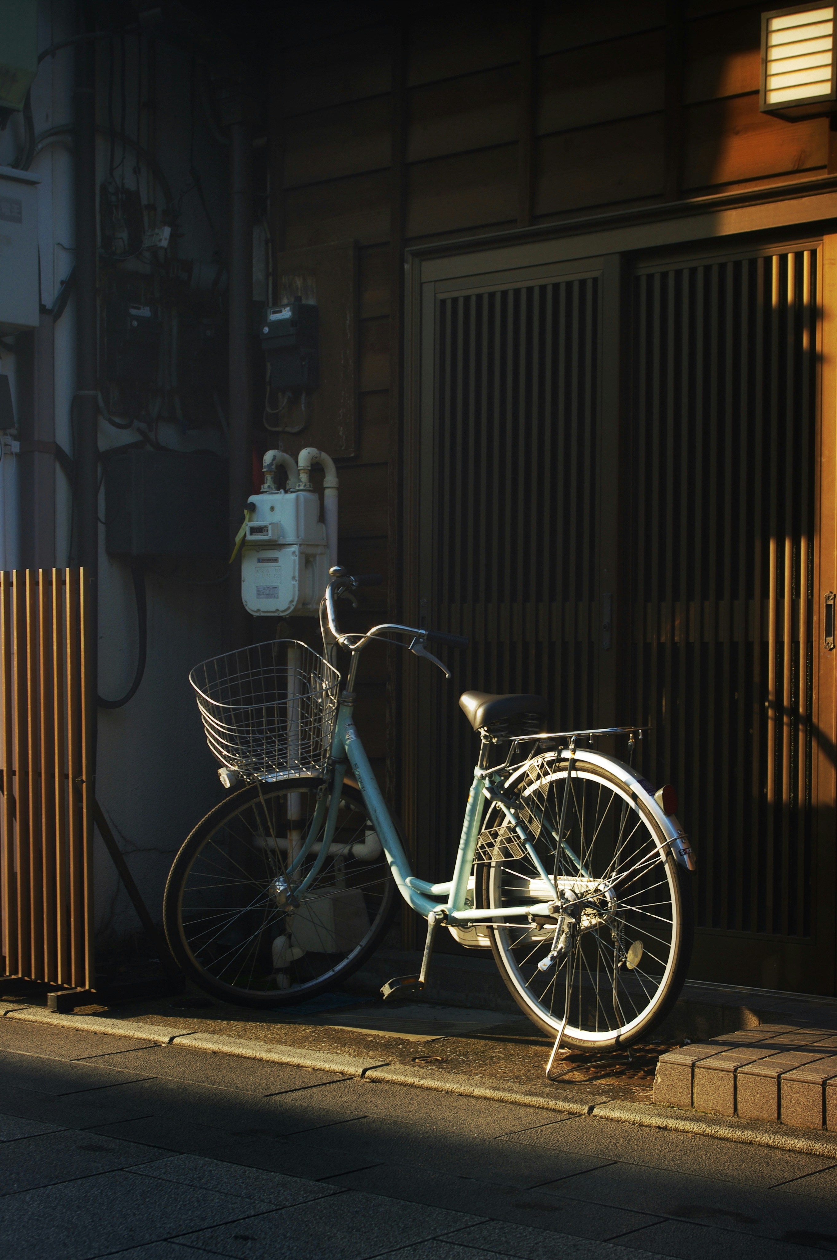 A pastel blue bicycle rests quietly against a wooden facade, bathed in soft golden evening light. A peaceful moment on a quiet Japanese street, blending everyday life with nostalgic beauty. | A bicycle leans against a wooden building.