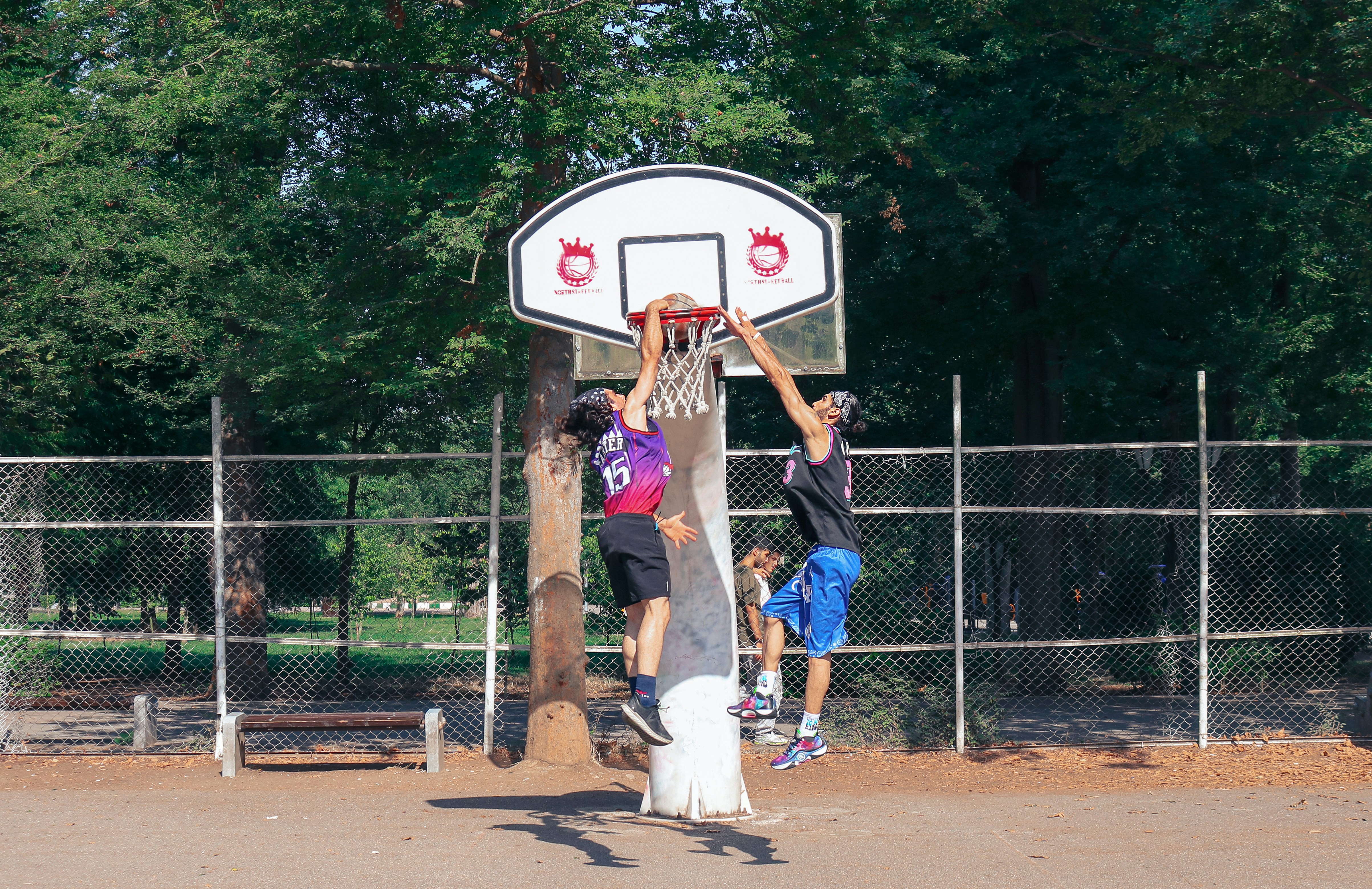 Two people play basketball at an outdoor court.