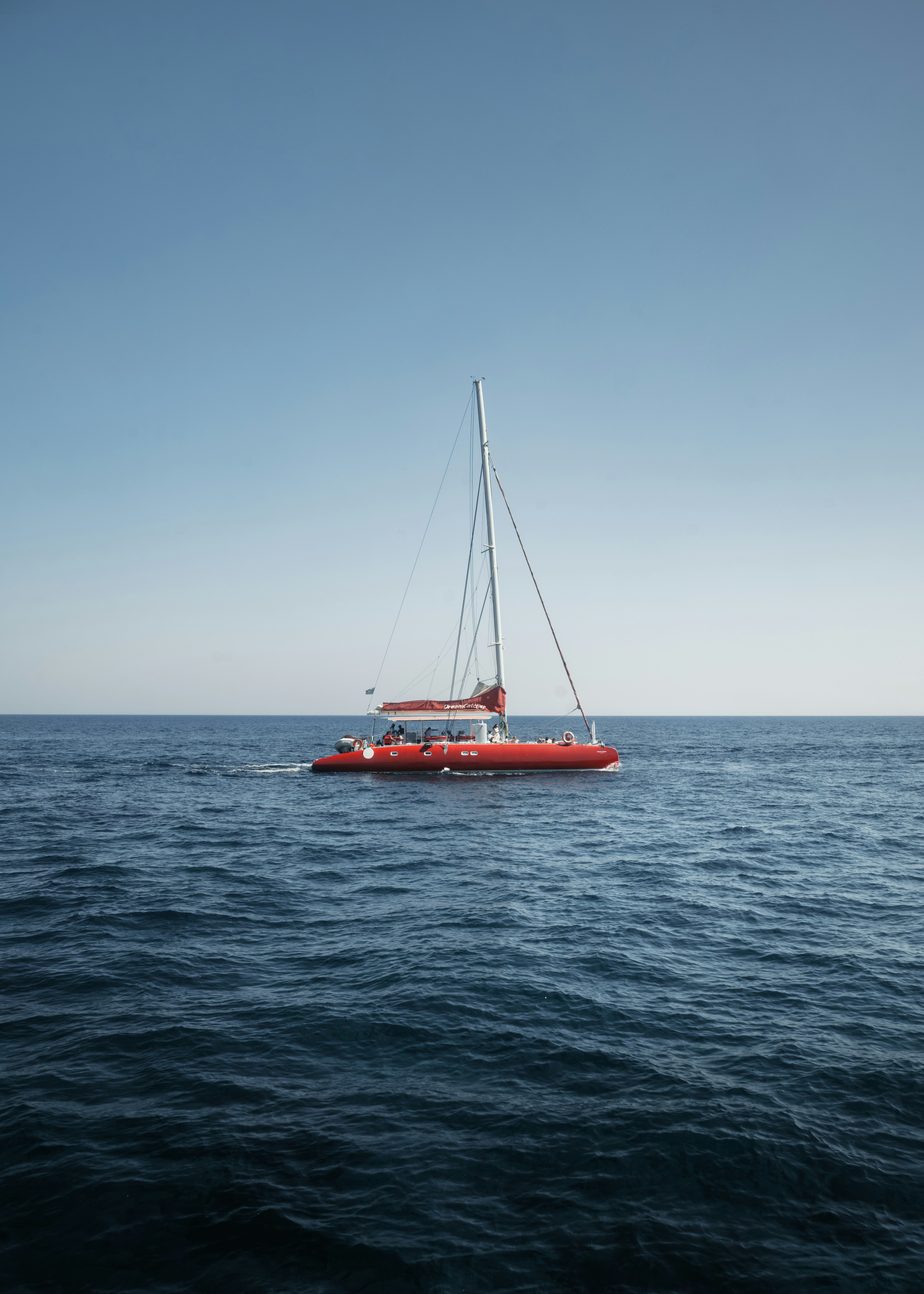 A red sailboat floats on the calm blue ocean.