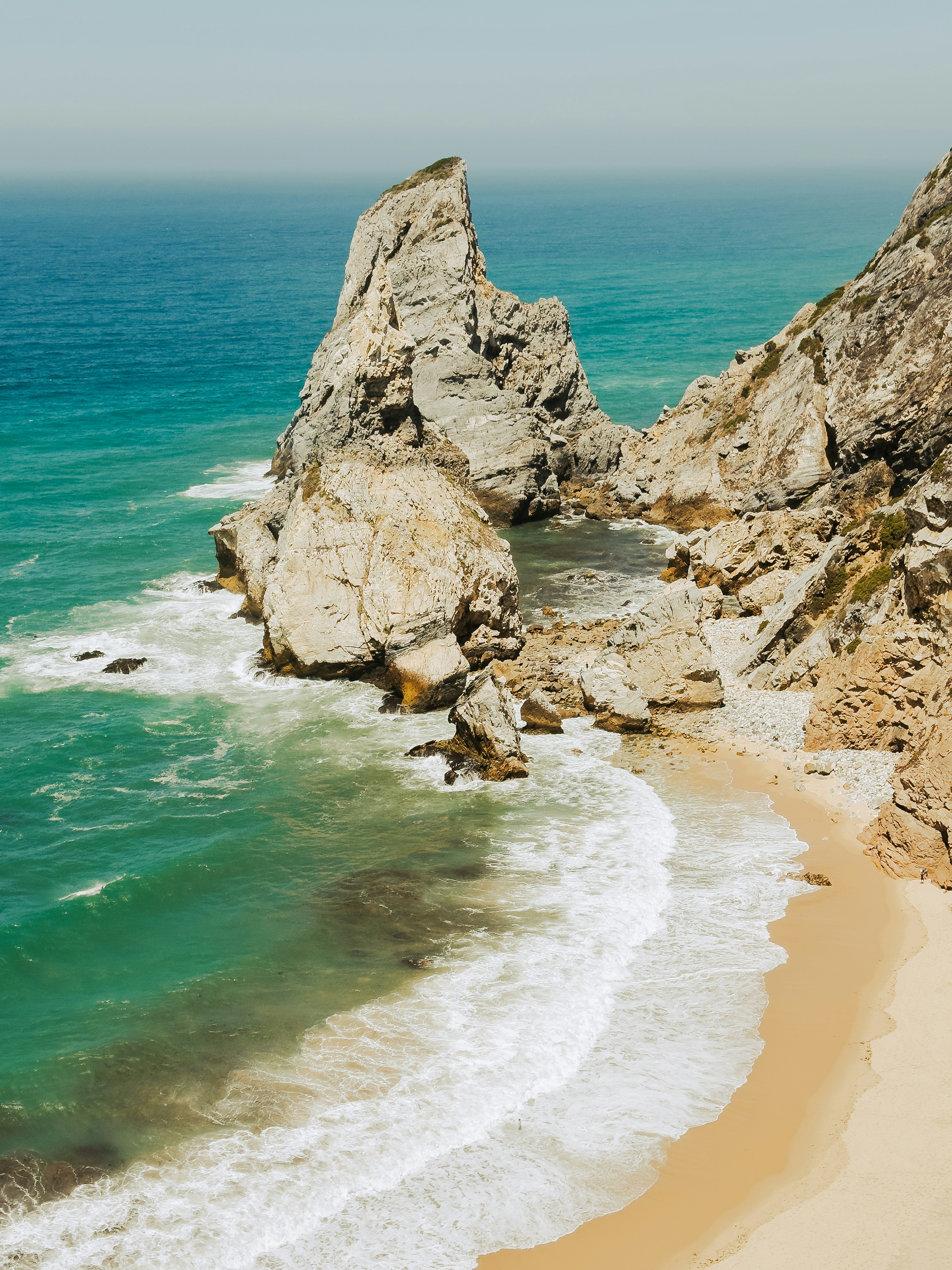 Rocky cliffs meet the ocean and sandy beach.