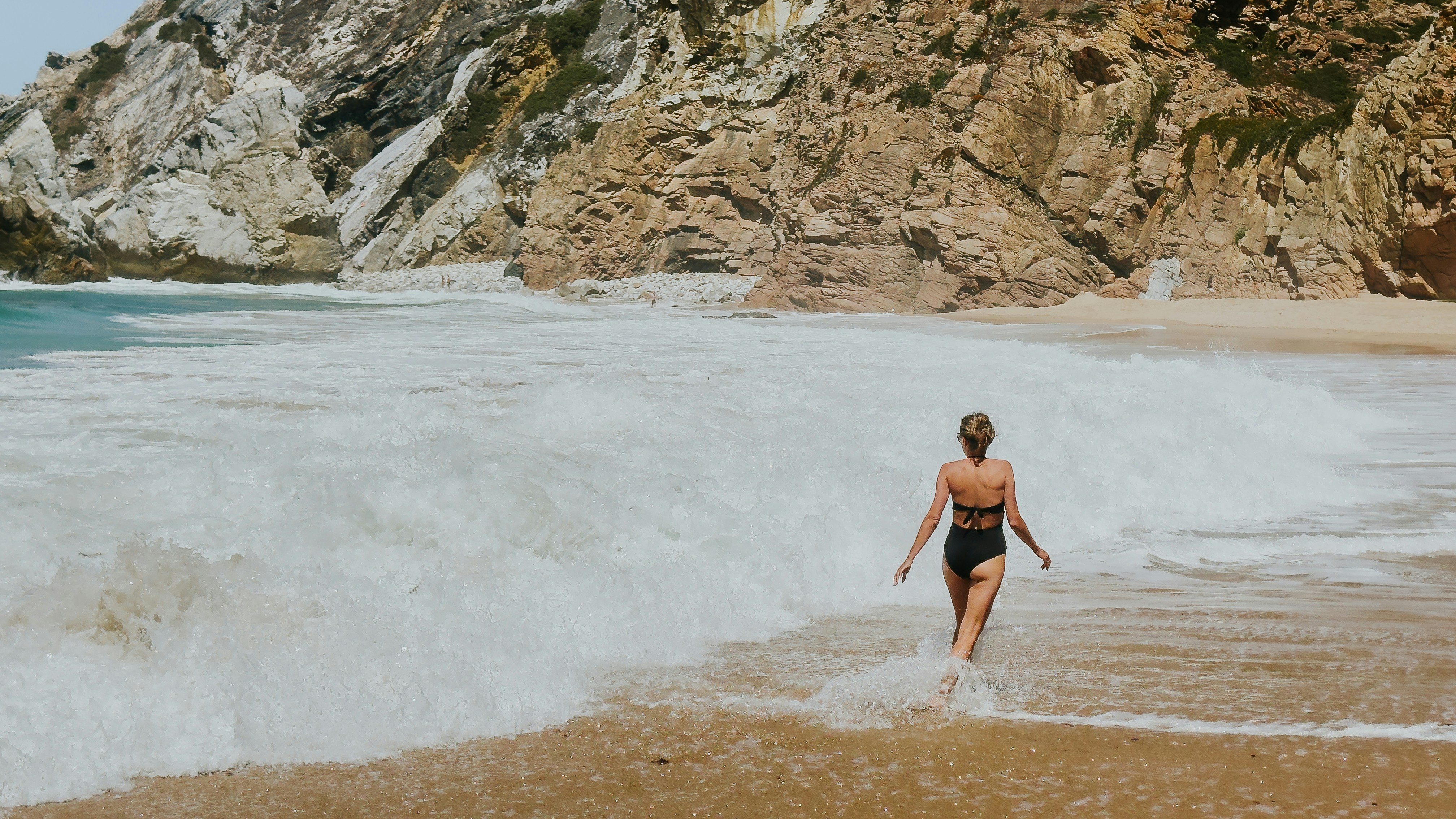 Woman walks into the ocean on a sunny beach.