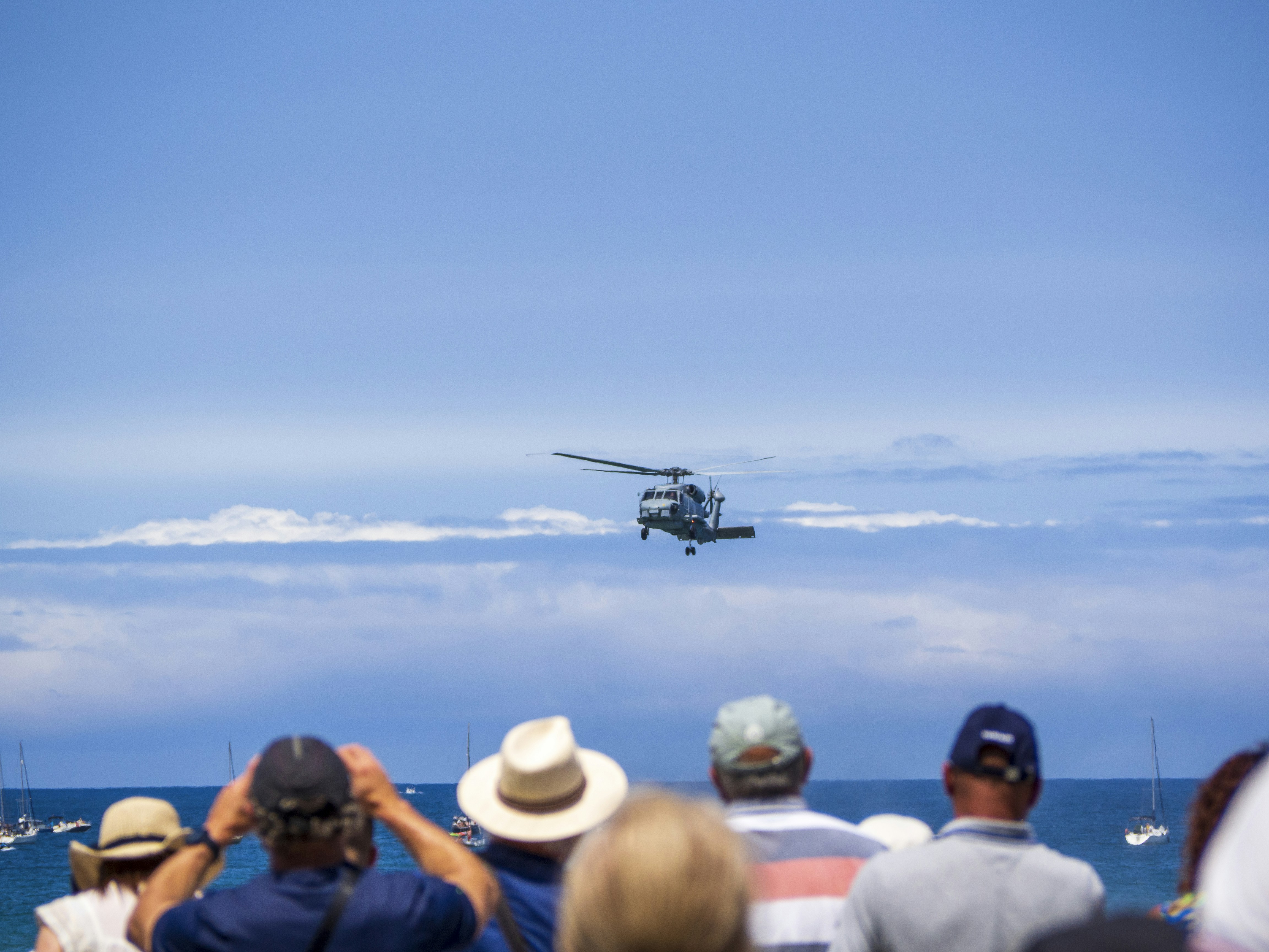 Blue Horizon Hover: Crowd Watches a Low-Altitude Helicopter Glide Over the Sea