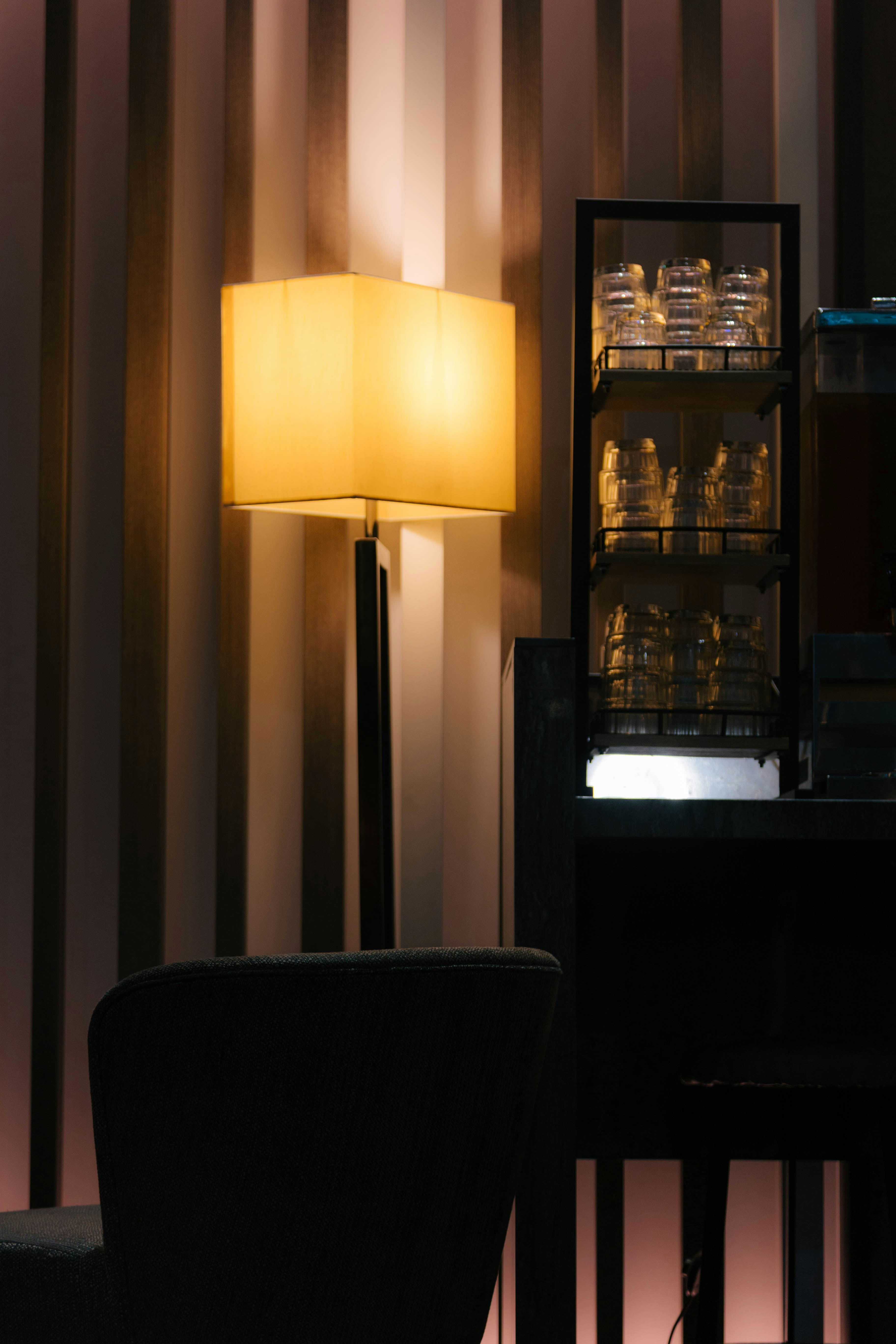 A cozy lamp illuminates a stylish café setting, complemented by glassware on display. The background features elegant vertical stripes in soft hues.
