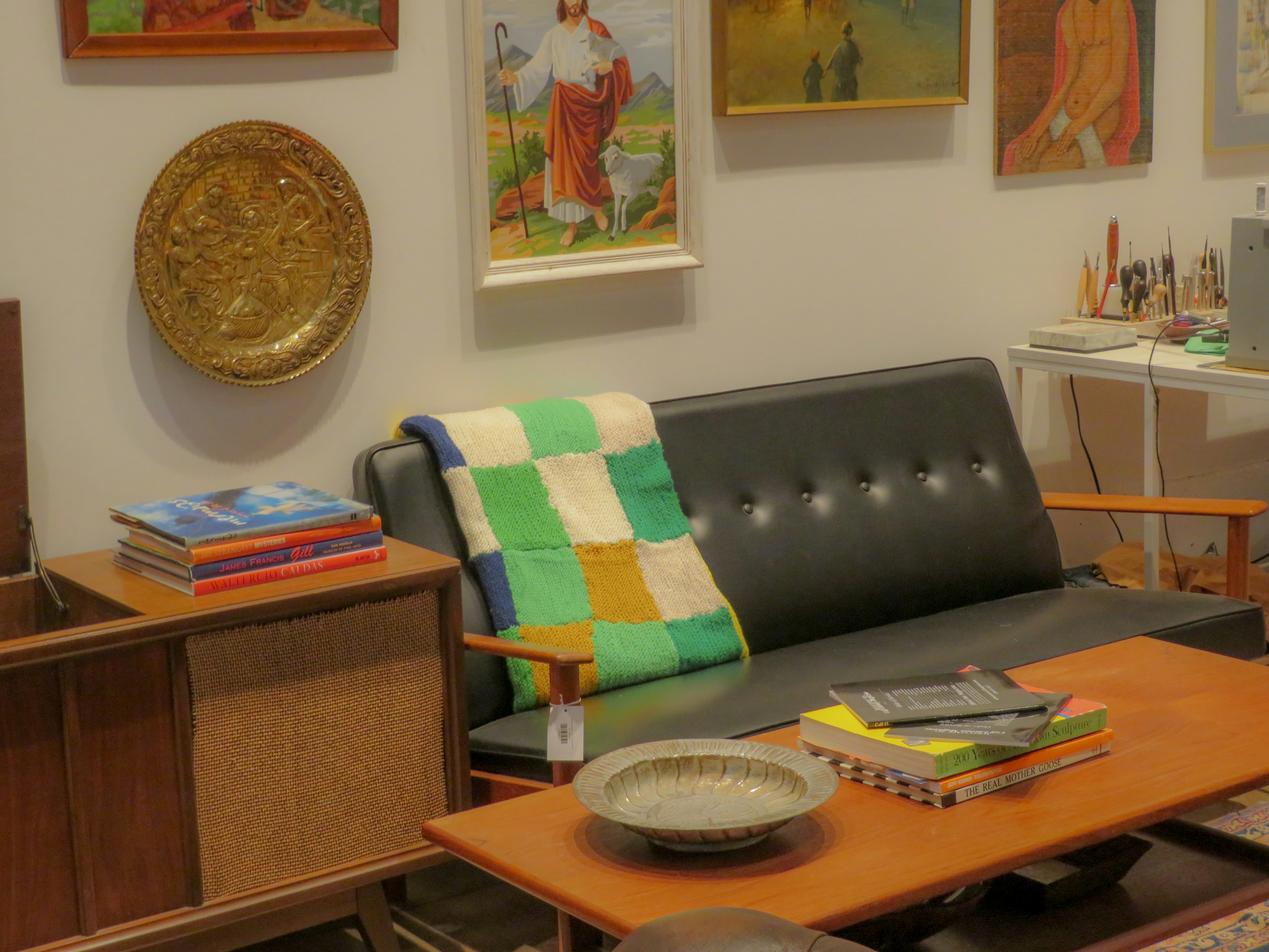 Mid-century modern living room featuring a sleek black sofa adorned with a colorful blanket, surrounded by eclectic artwork and books. The scene invites relaxation and creativity.