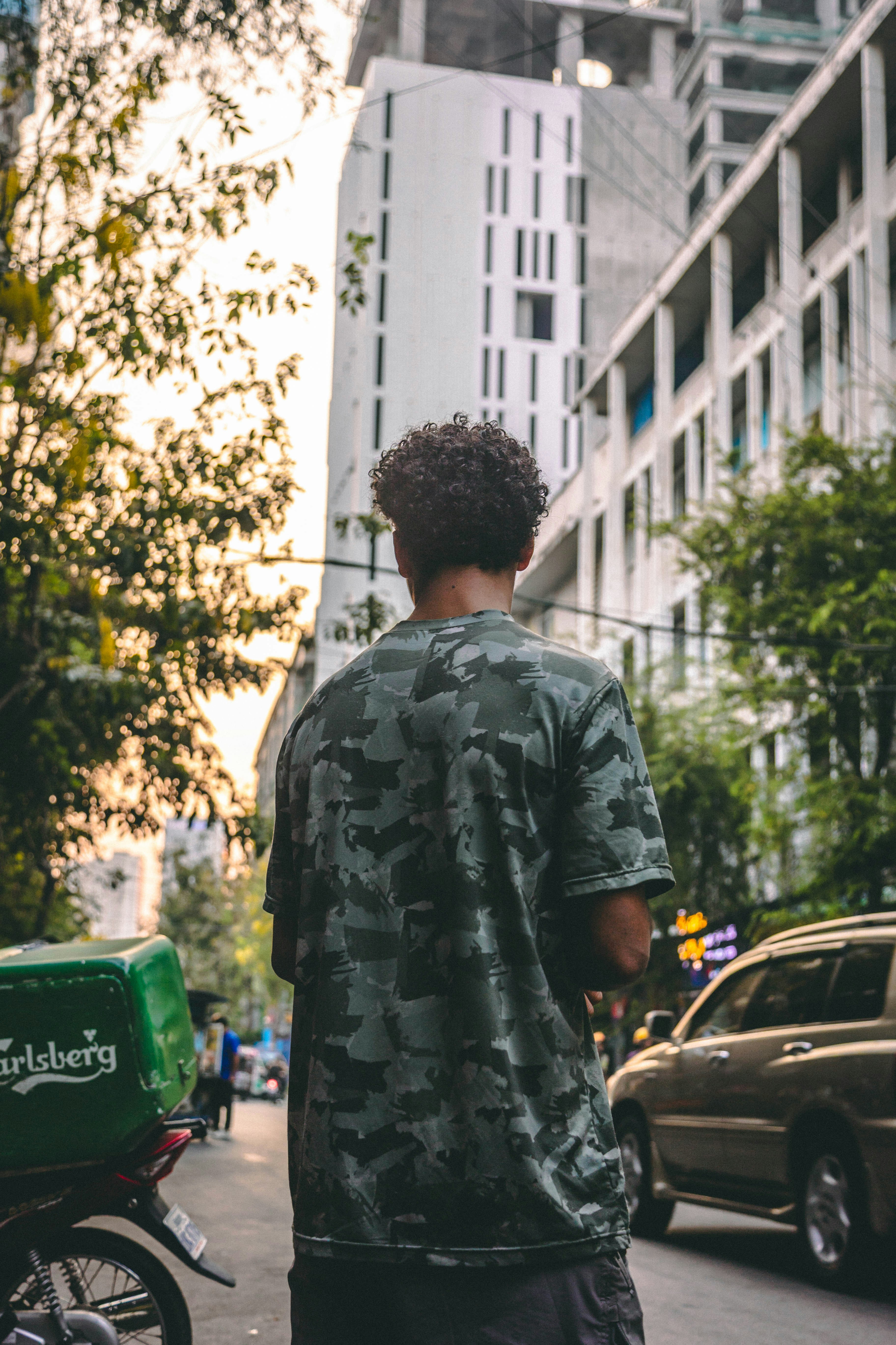 Man in camouflage shirt looks at city buildings.