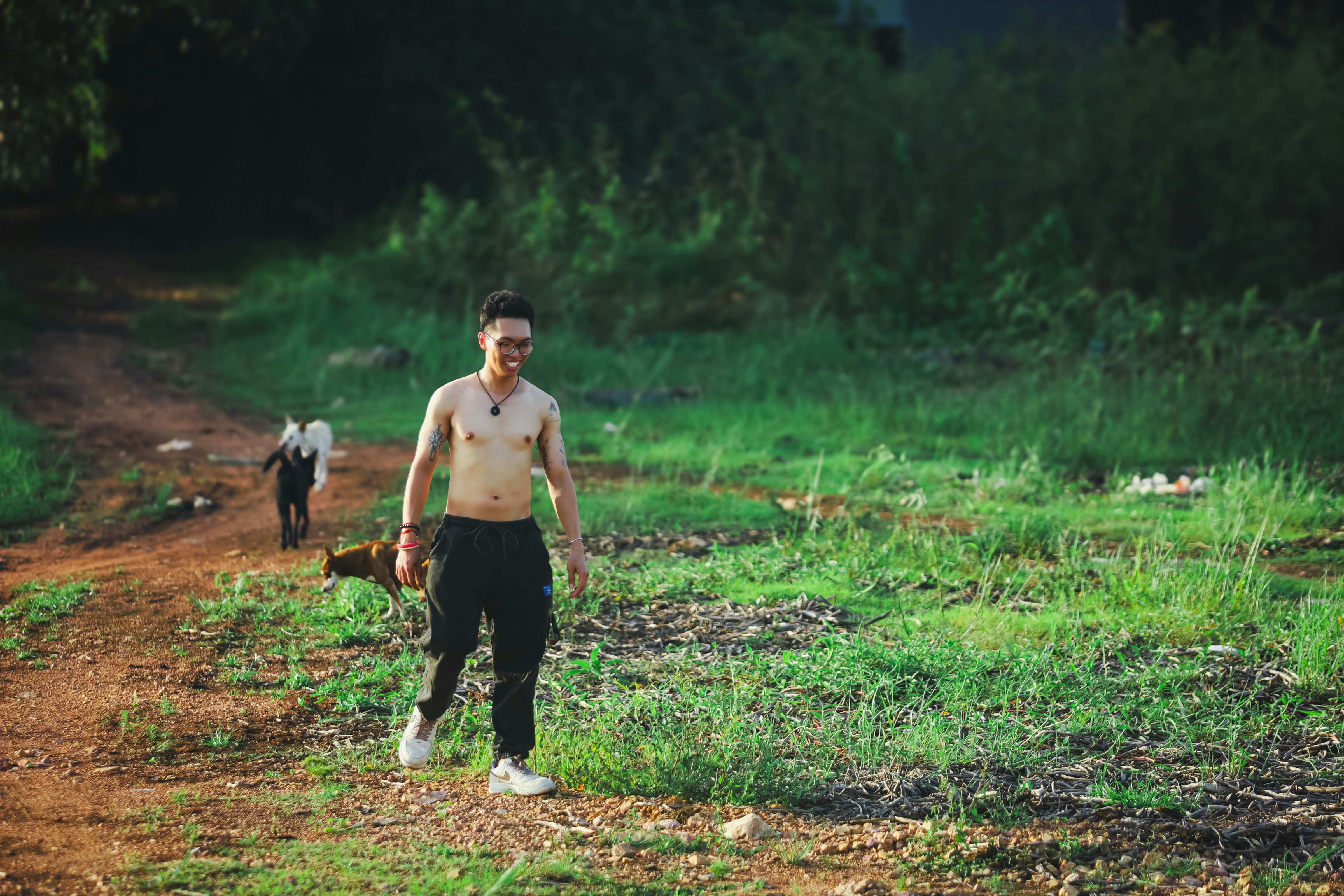 A shirtless man walks through a grassy field.