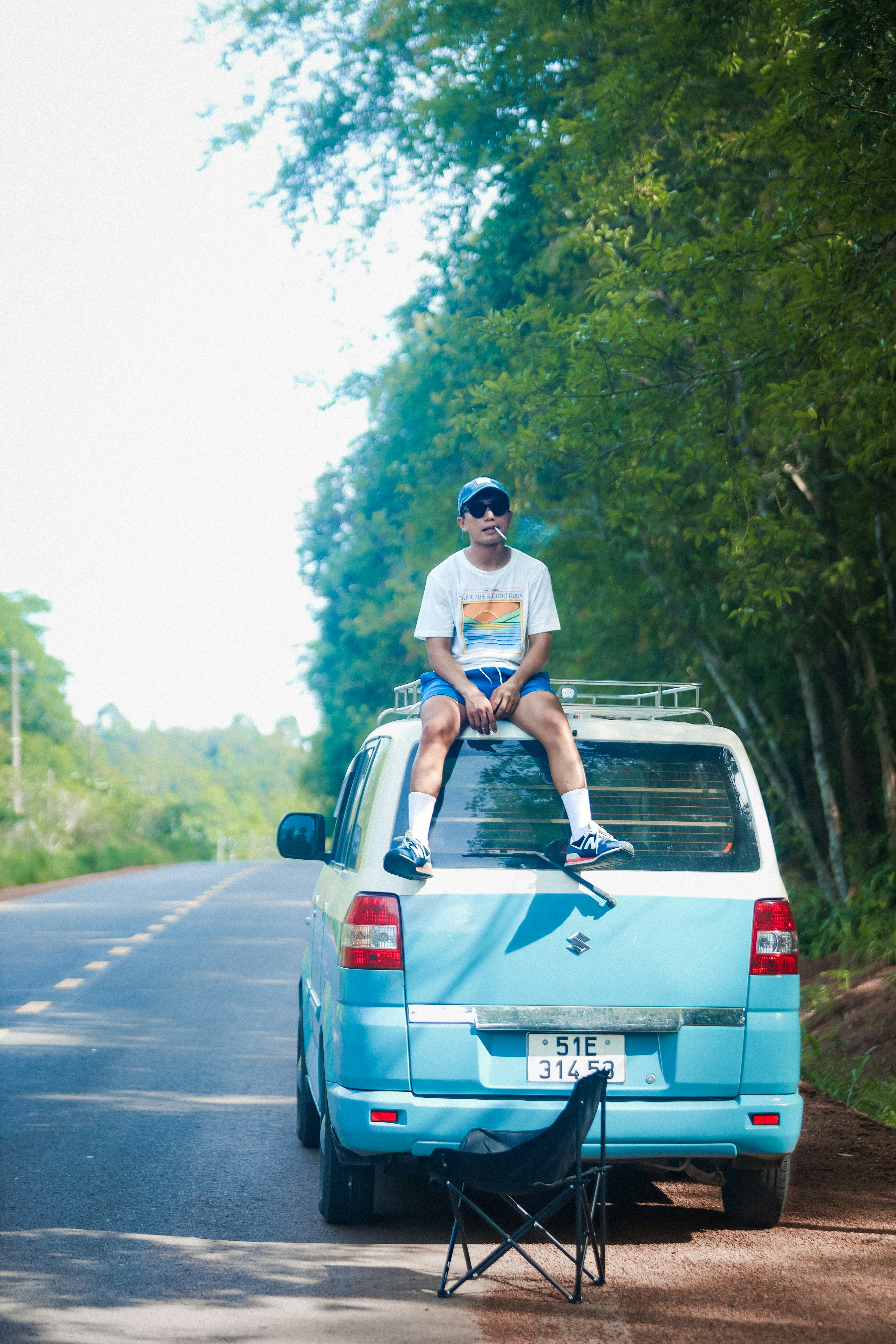 Man sits atop a van and smokes a cigarette.