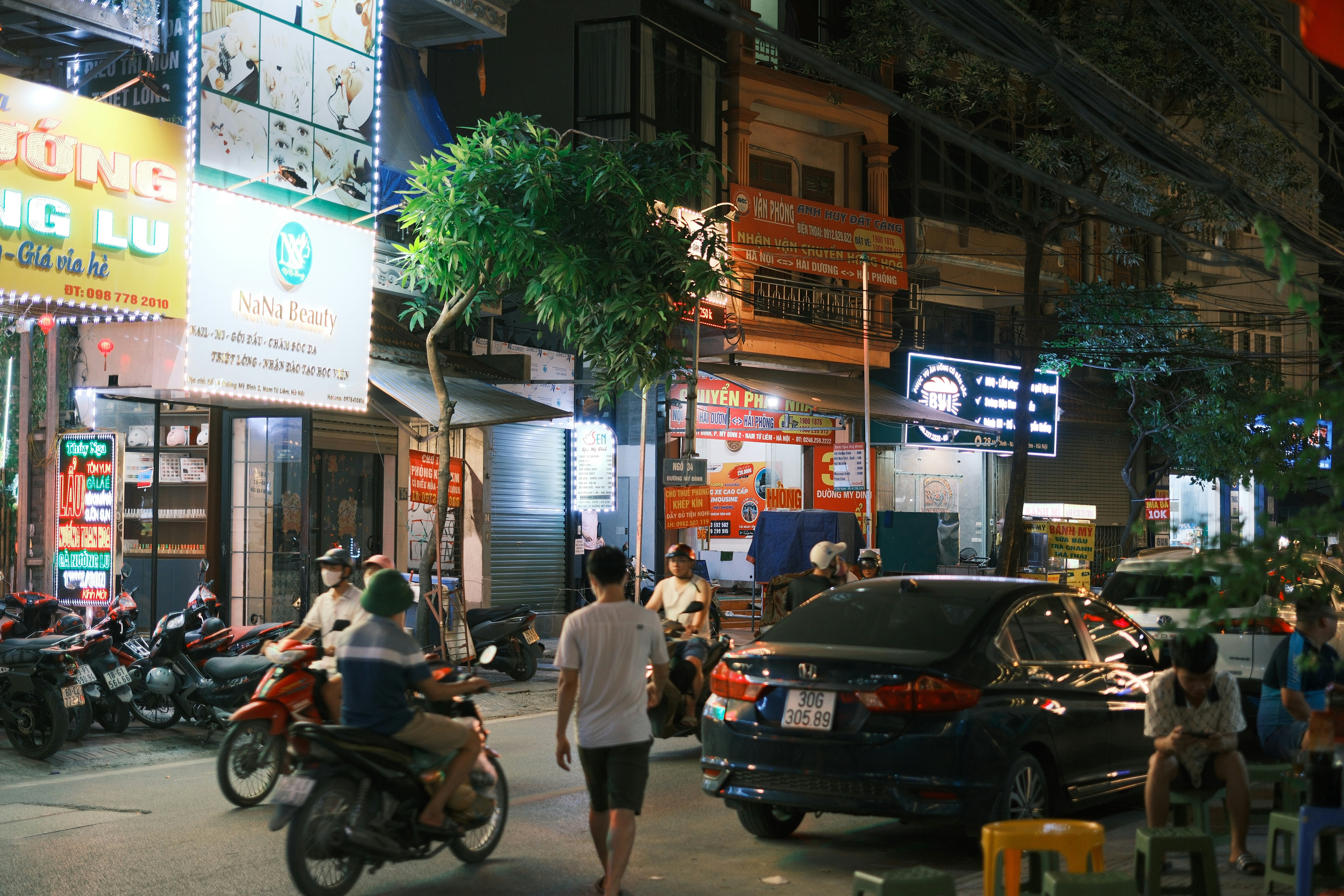 A bustling street scene at night, featuring a mix of vehicles and pedestrians amid vibrant neon signs and storefronts.