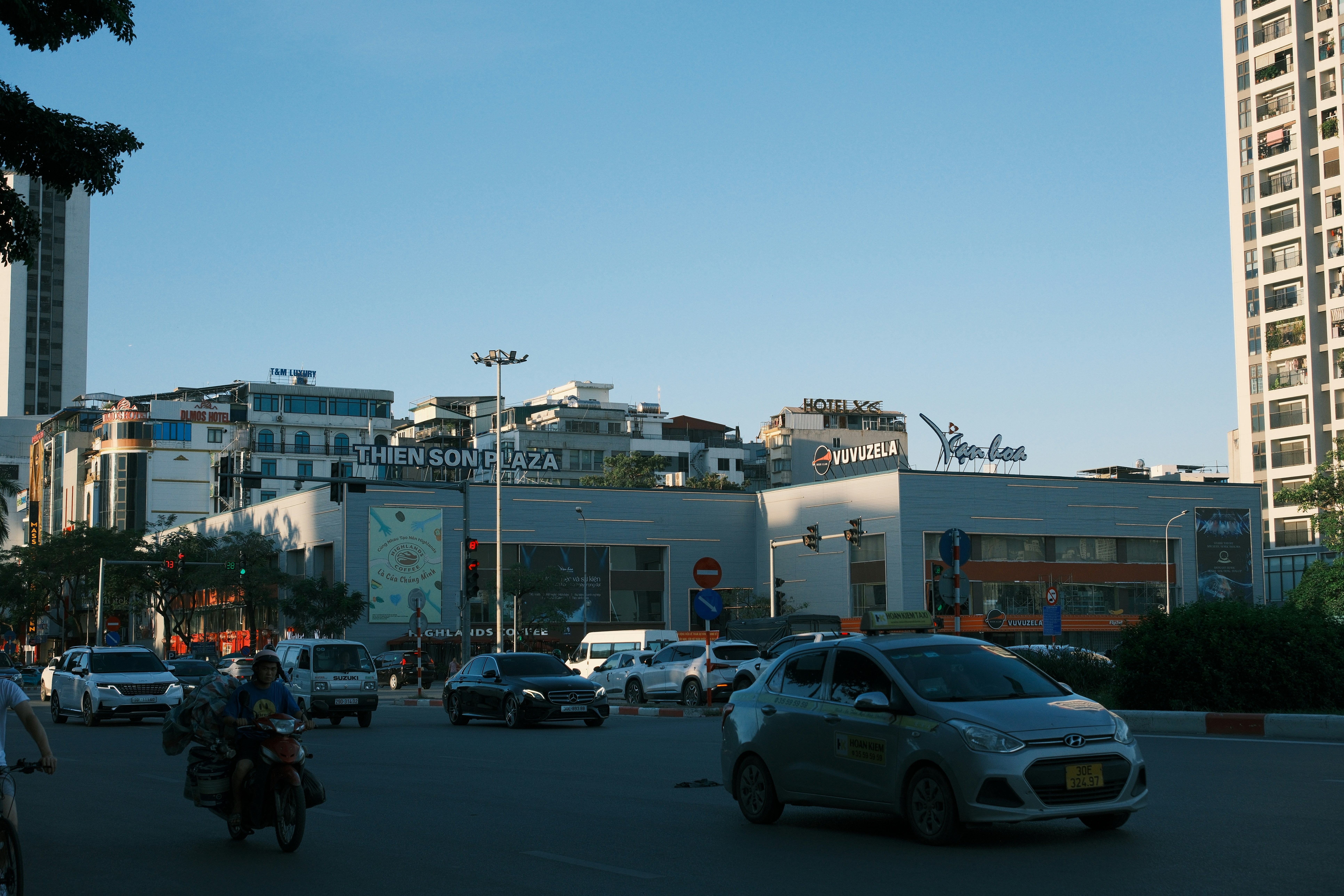 Cars drive on a city street with buildings.