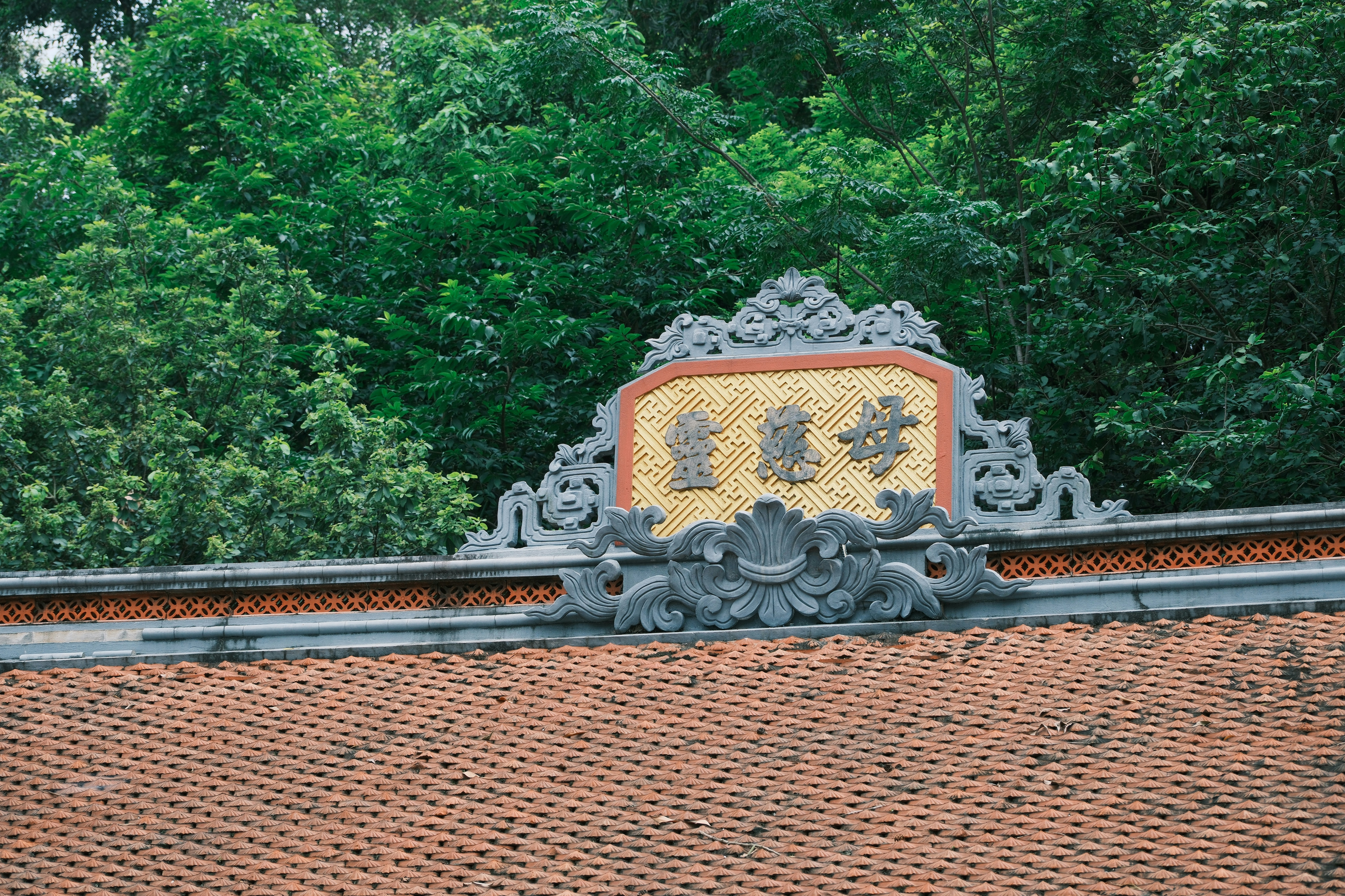 A sign adorns a temple roof with forest in the background.