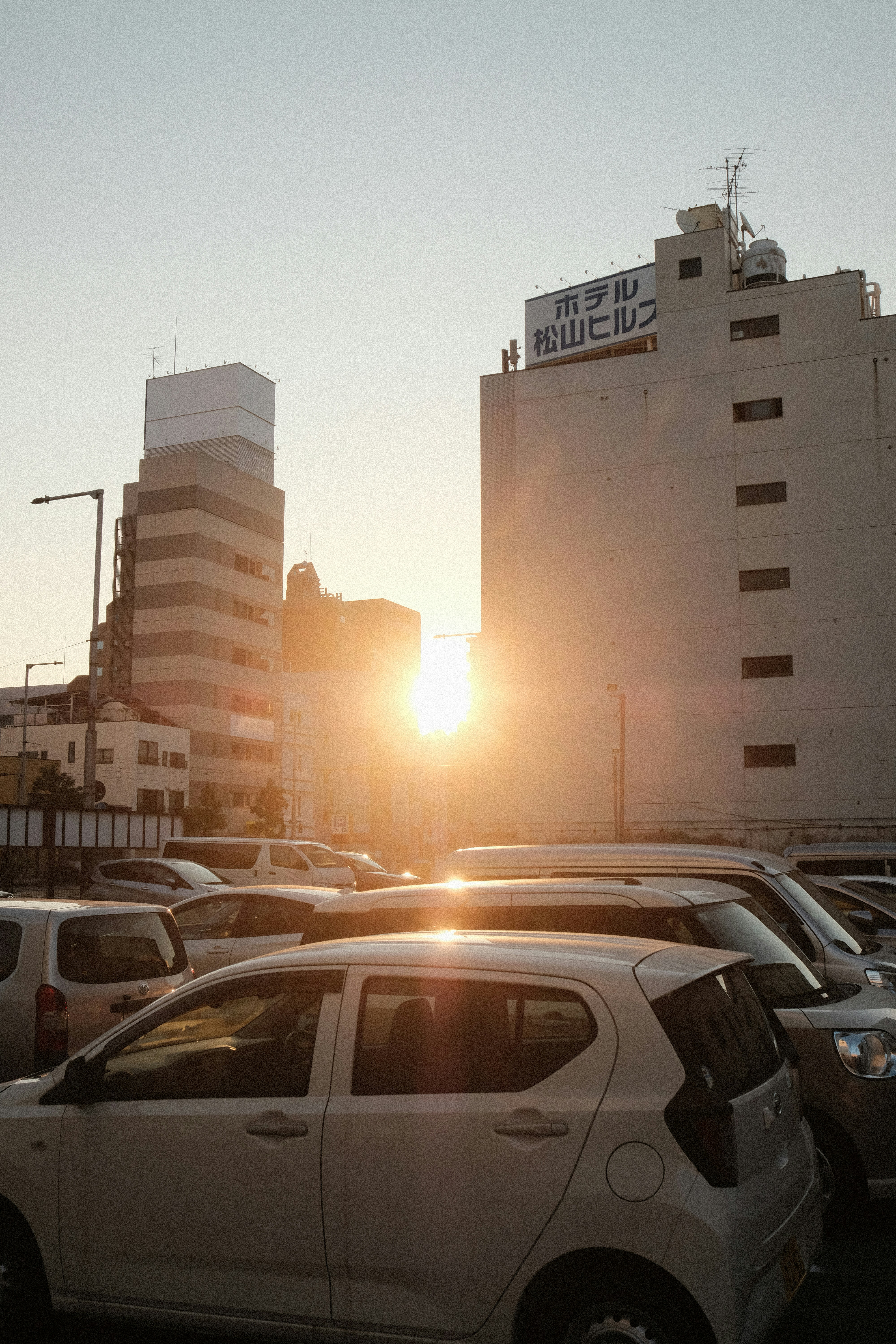 Golden sunlight gleams through a gap between buildings, illuminating parked cars in an urban setting.