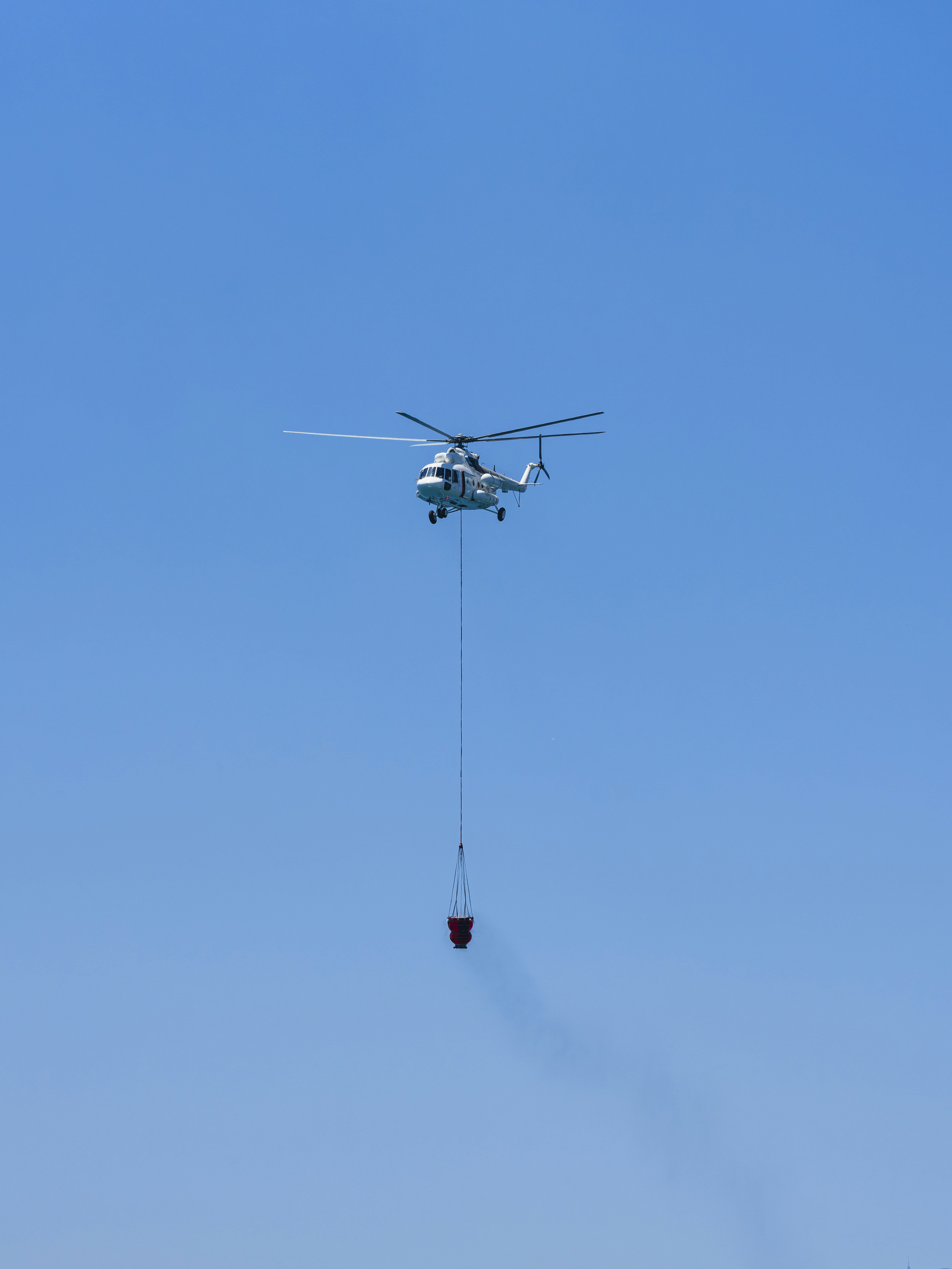 Aerial Hose Drop: Helicopter Dangles a Fire Bucket Against a Clear Sky