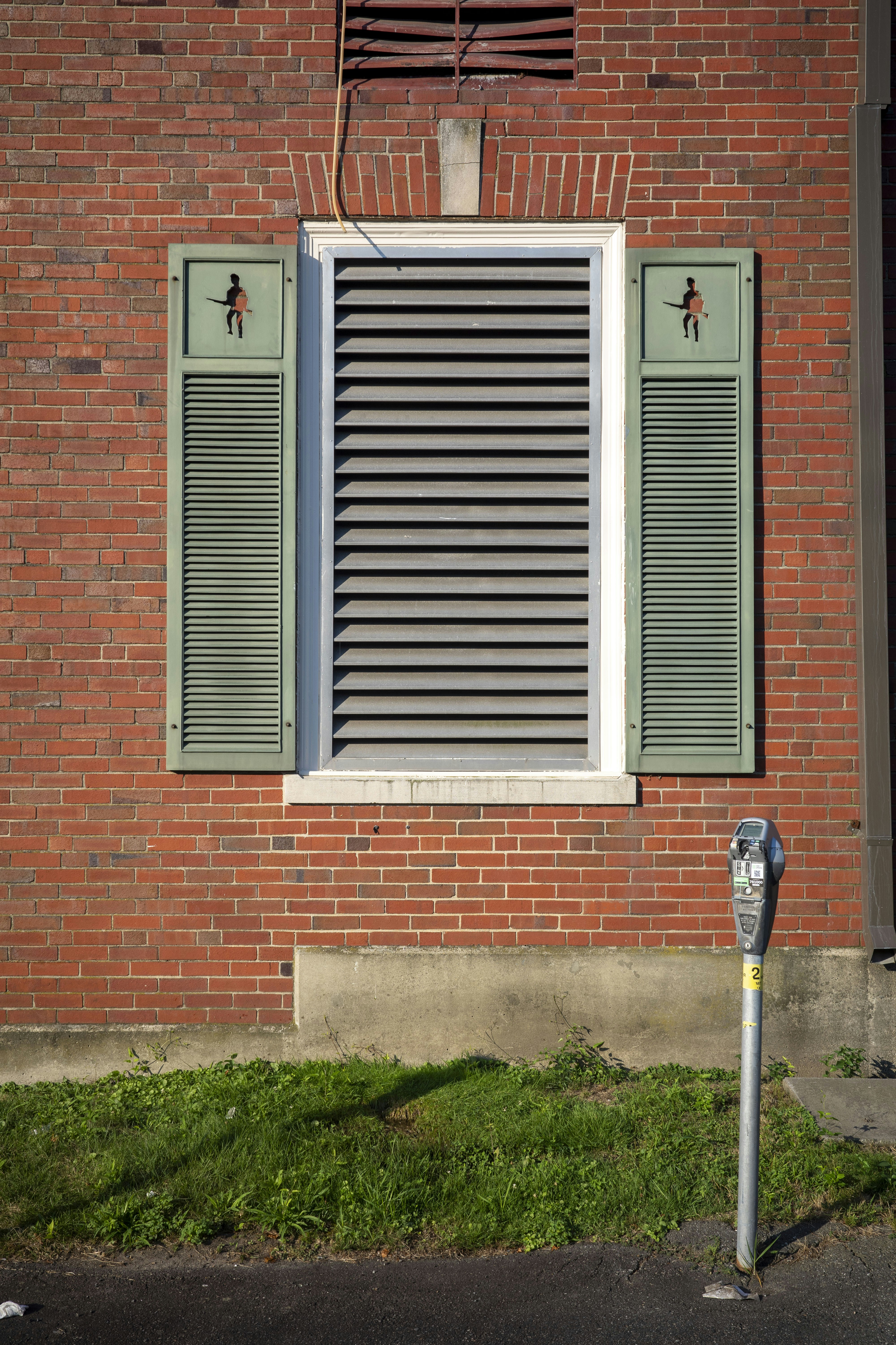 Urban Window Crown: Green Shutters Framing a Vented Window on Red Brick