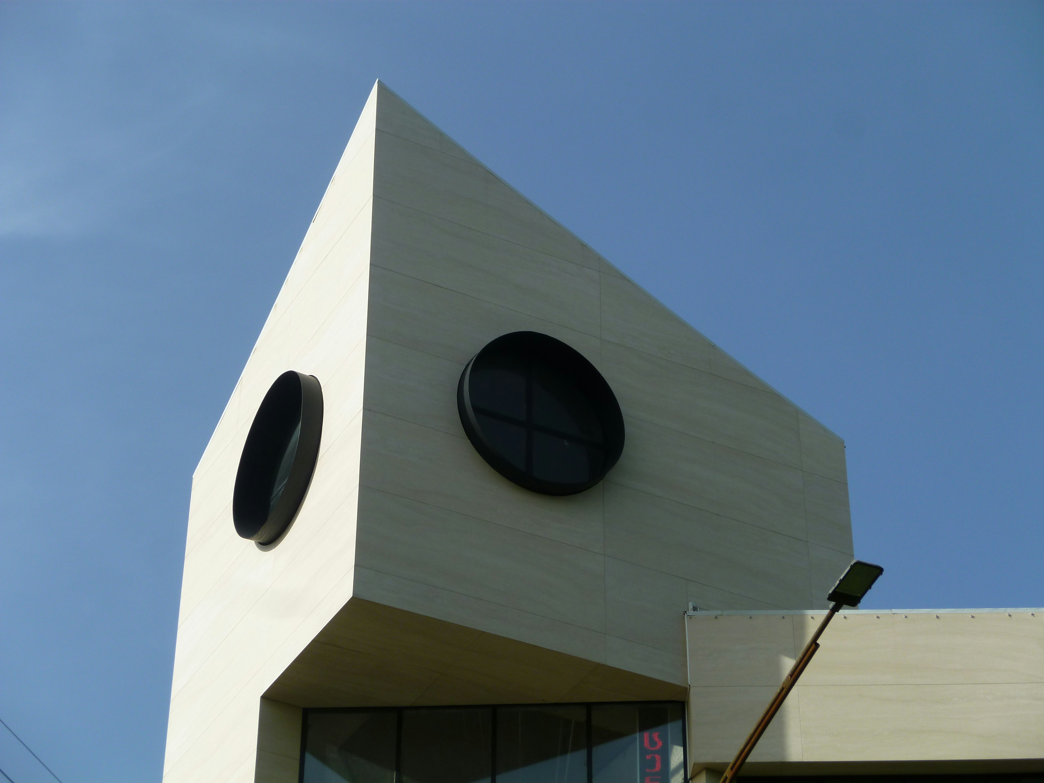Modern building corner featuring an angular design with circular windows against a clear blue sky.