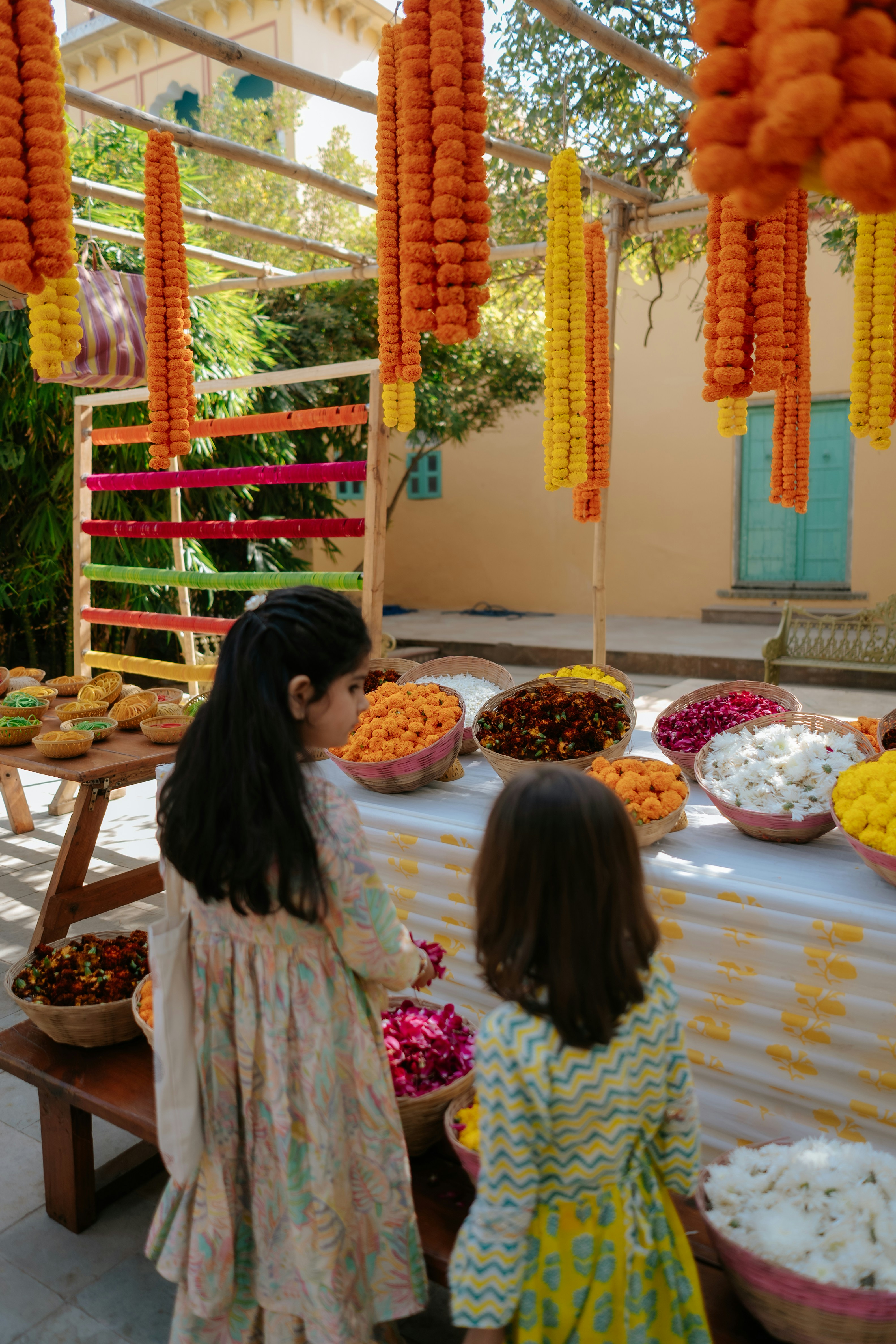 Two children exploring a vibrant market filled with colorful flower arrangements and decorative garlands. The scene captures the essence of local culture and festivity.