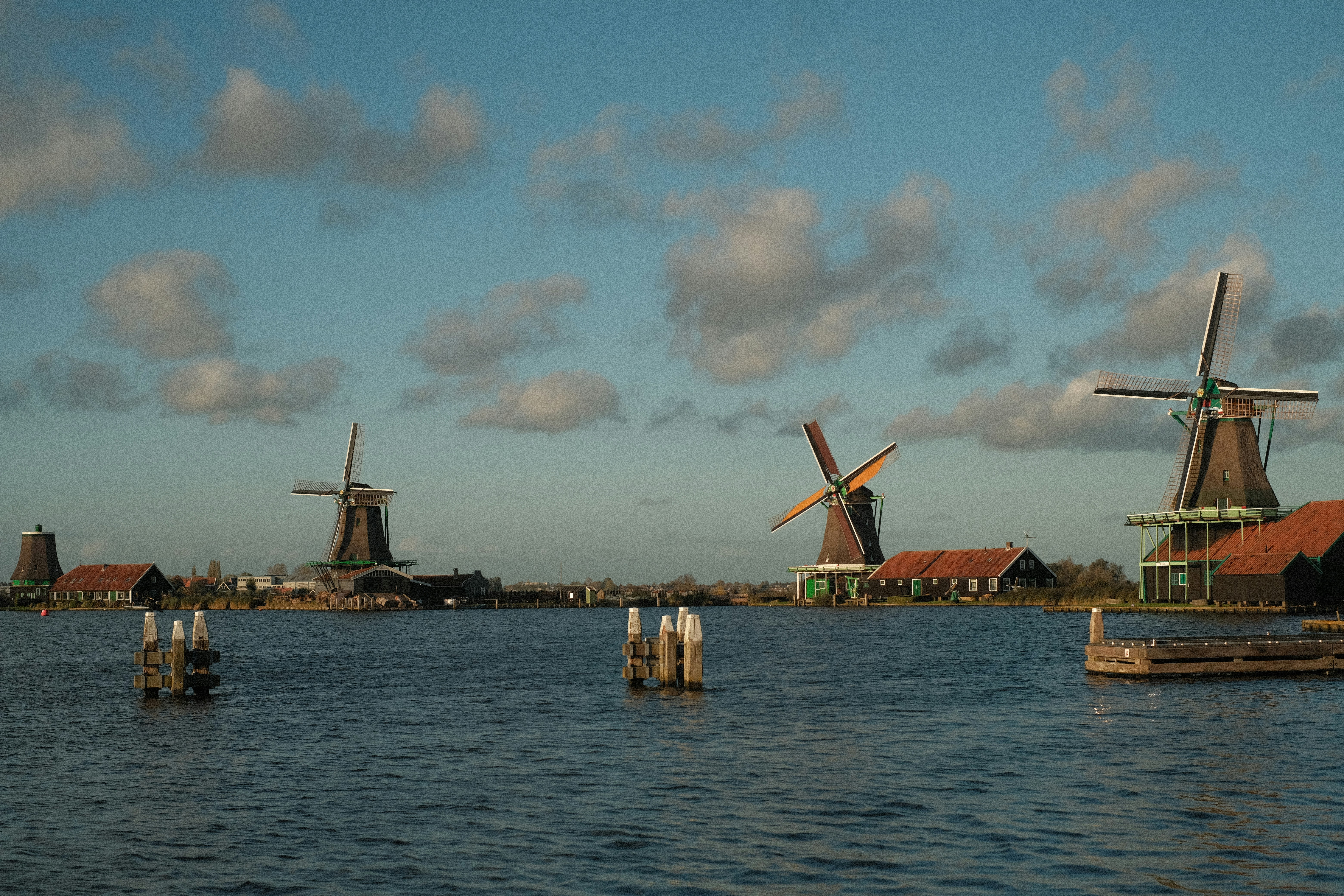 Historic windmills stand gracefully along the water's edge, framed by a clear blue sky and scattered clouds.