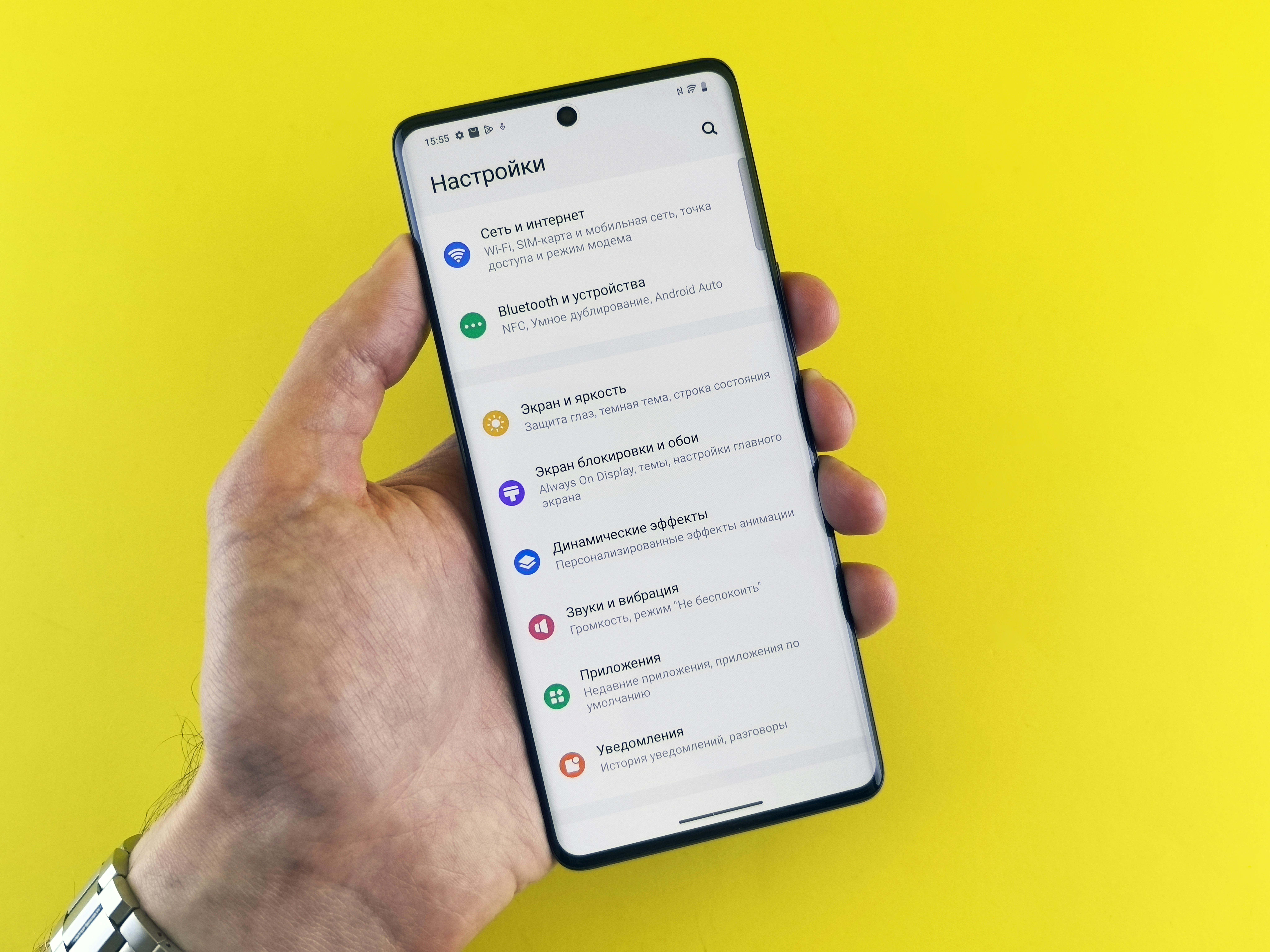 A hand holding a smartphone displaying settings in a vibrant yellow environment.