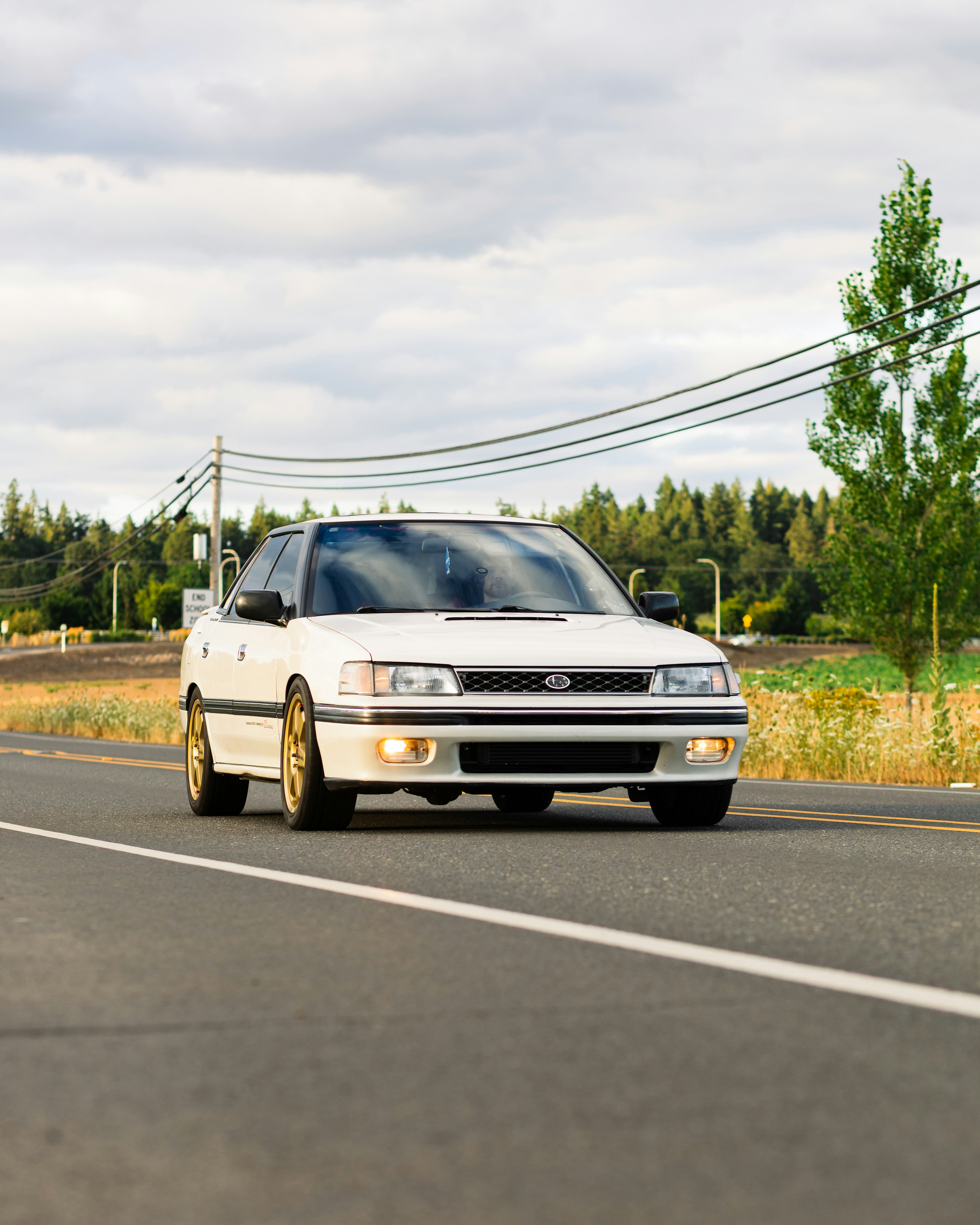 Rural Glide: White sedan on a sunlit two-lane road with distant fields