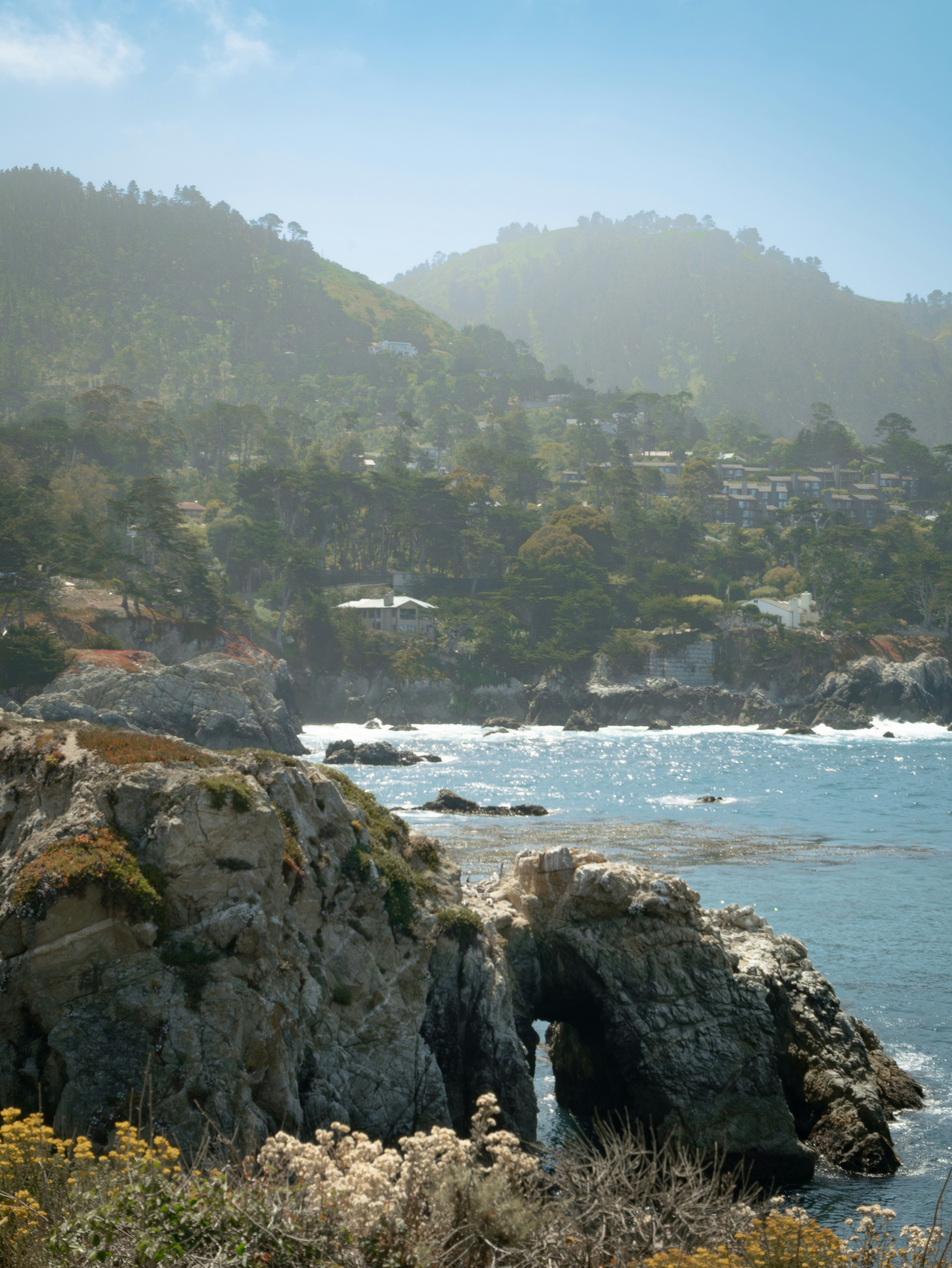 Rock Arch Reverie: Coastal Cliffs, Turquoise Sea, and a Distant Hillside Village